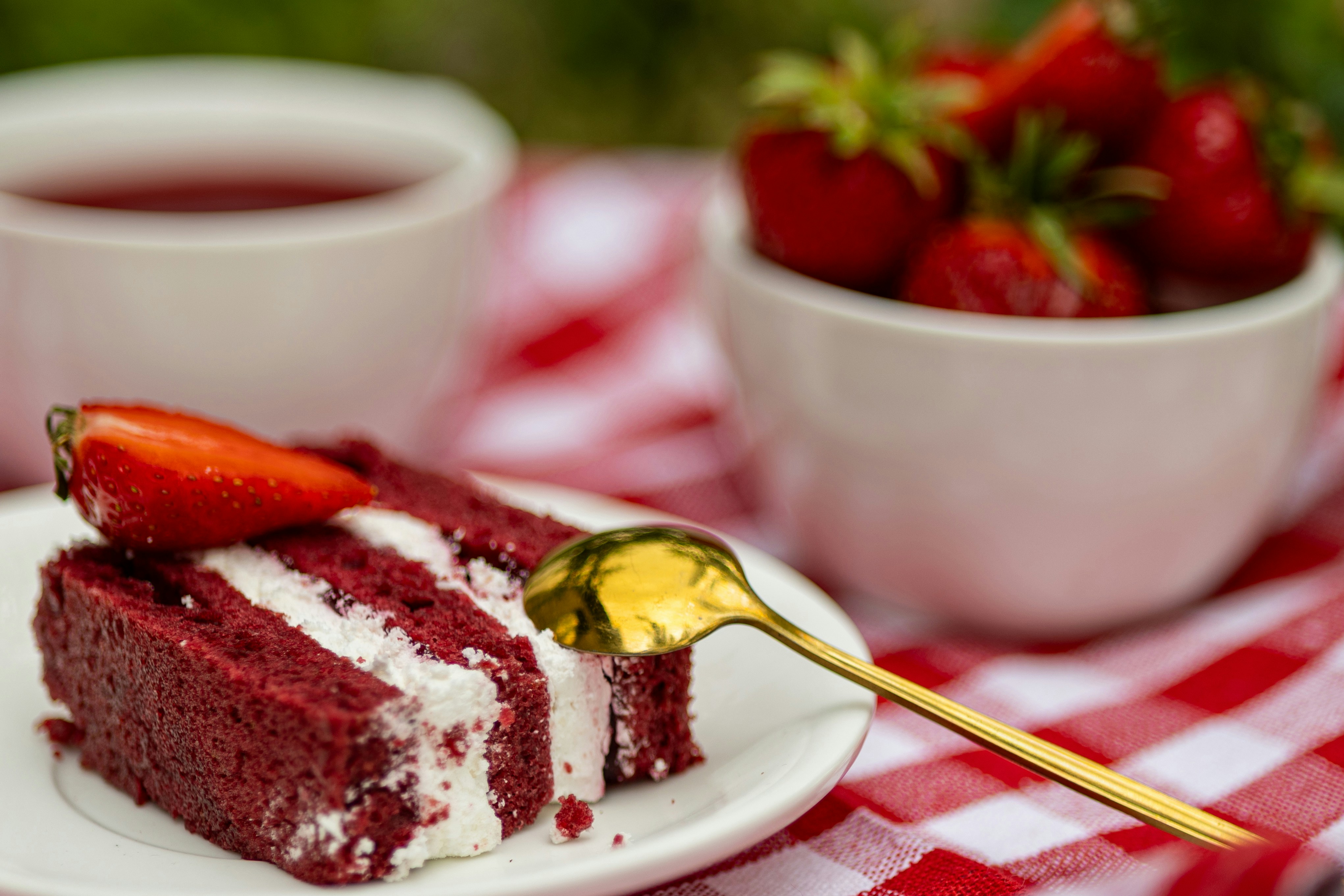 Strawberry-Drizzled Red Velvet Slice on Checkered Table, with Fresh Berries in the Background