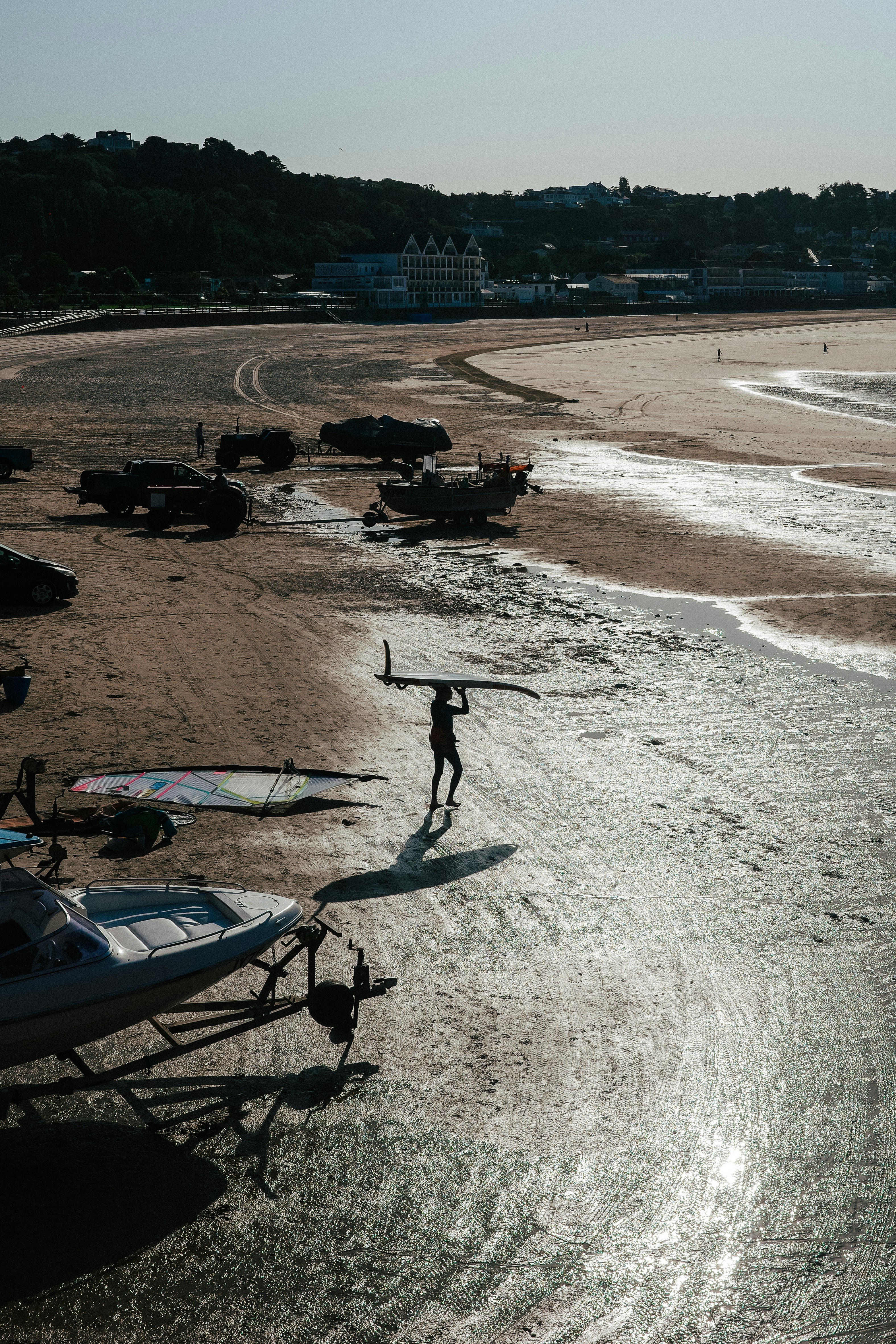 Person carrying surfboard on a sandy beach at low tide.