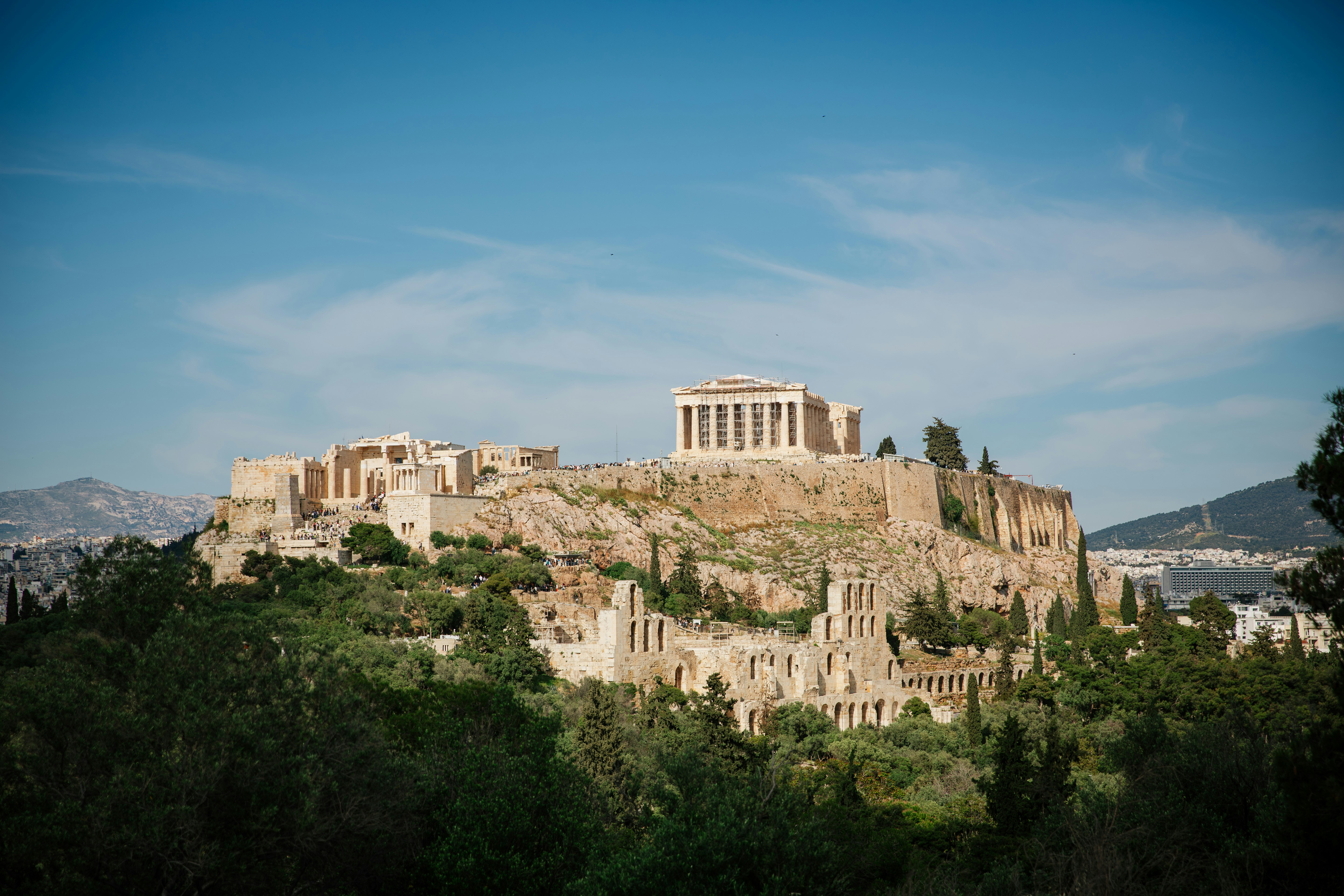Acropolis atop a sunlit hillside: ancient ruins amid olive and pine