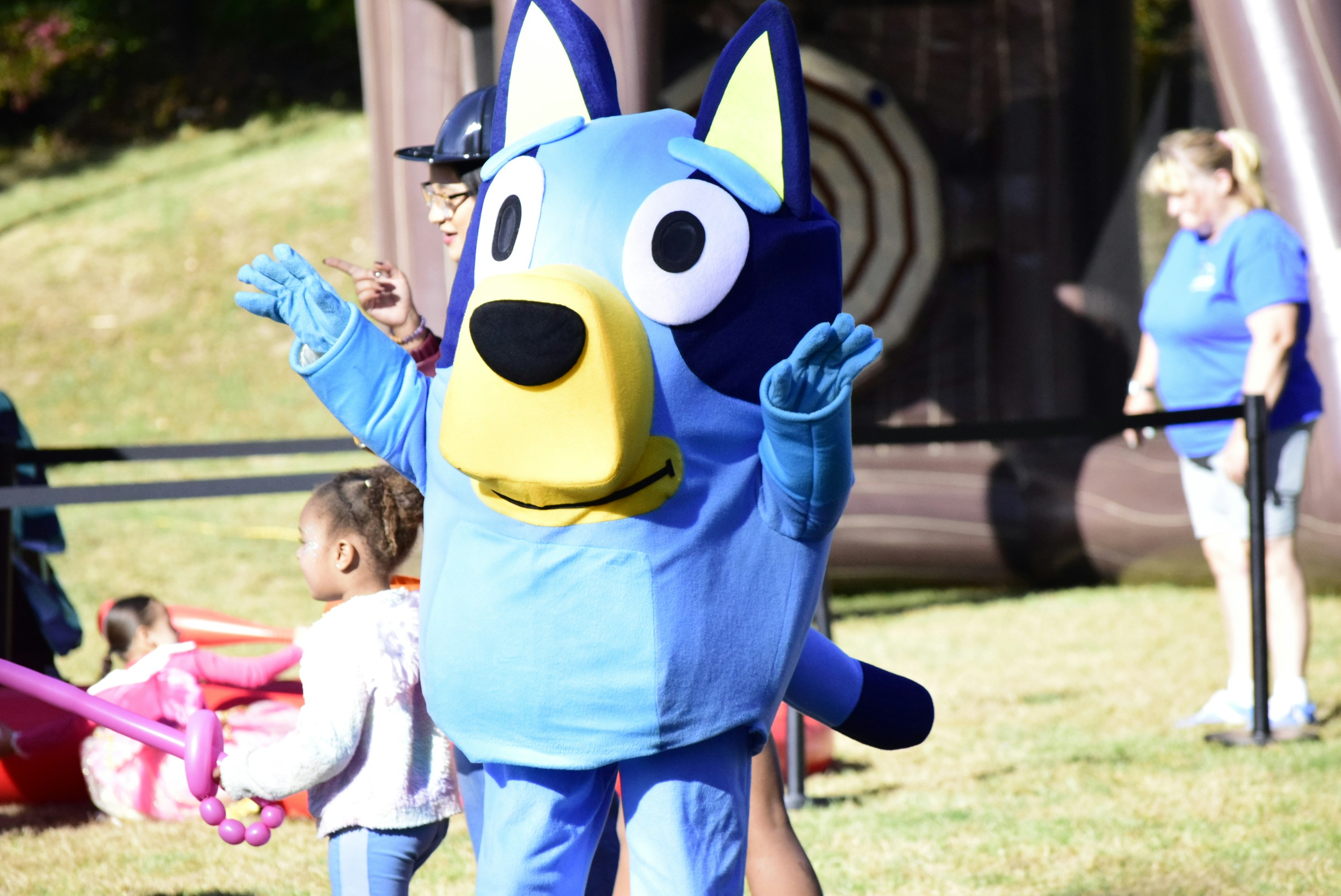 Blue mascot with raised arms at a daytime outdoor event