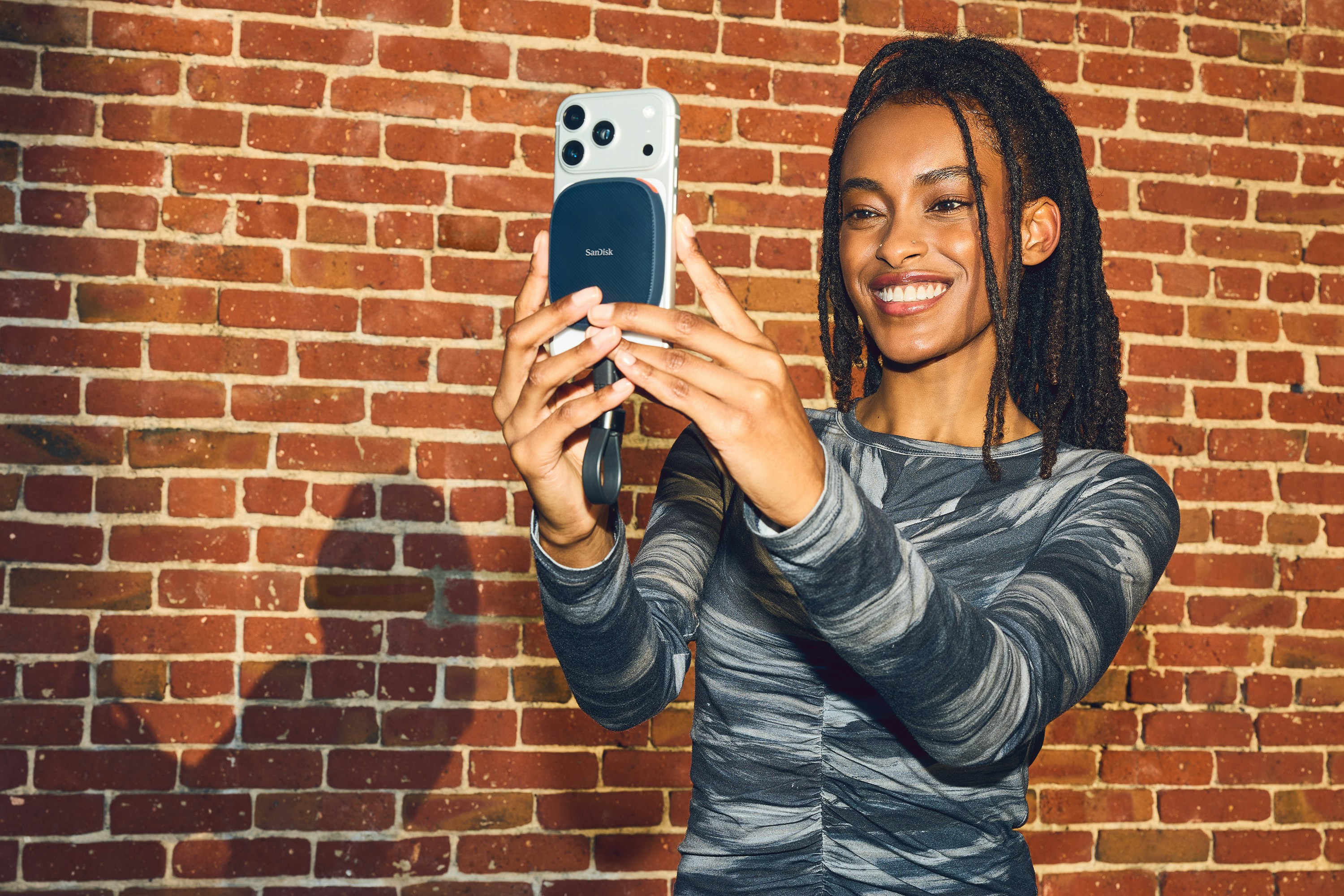 Smiling woman takes a selfie with smartphone against brick wall.