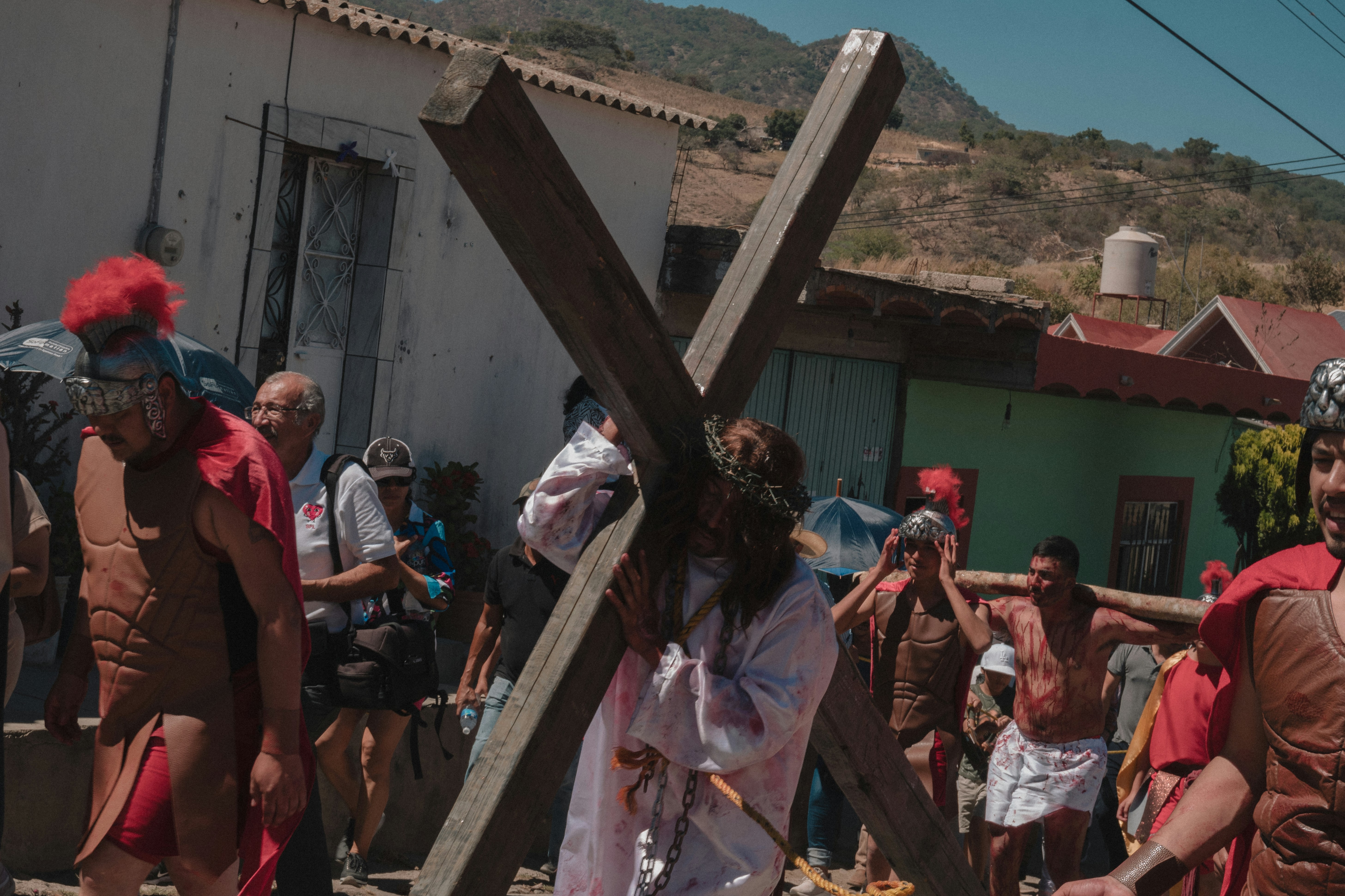 Man portraying jesus carrying a wooden cross in a procession.