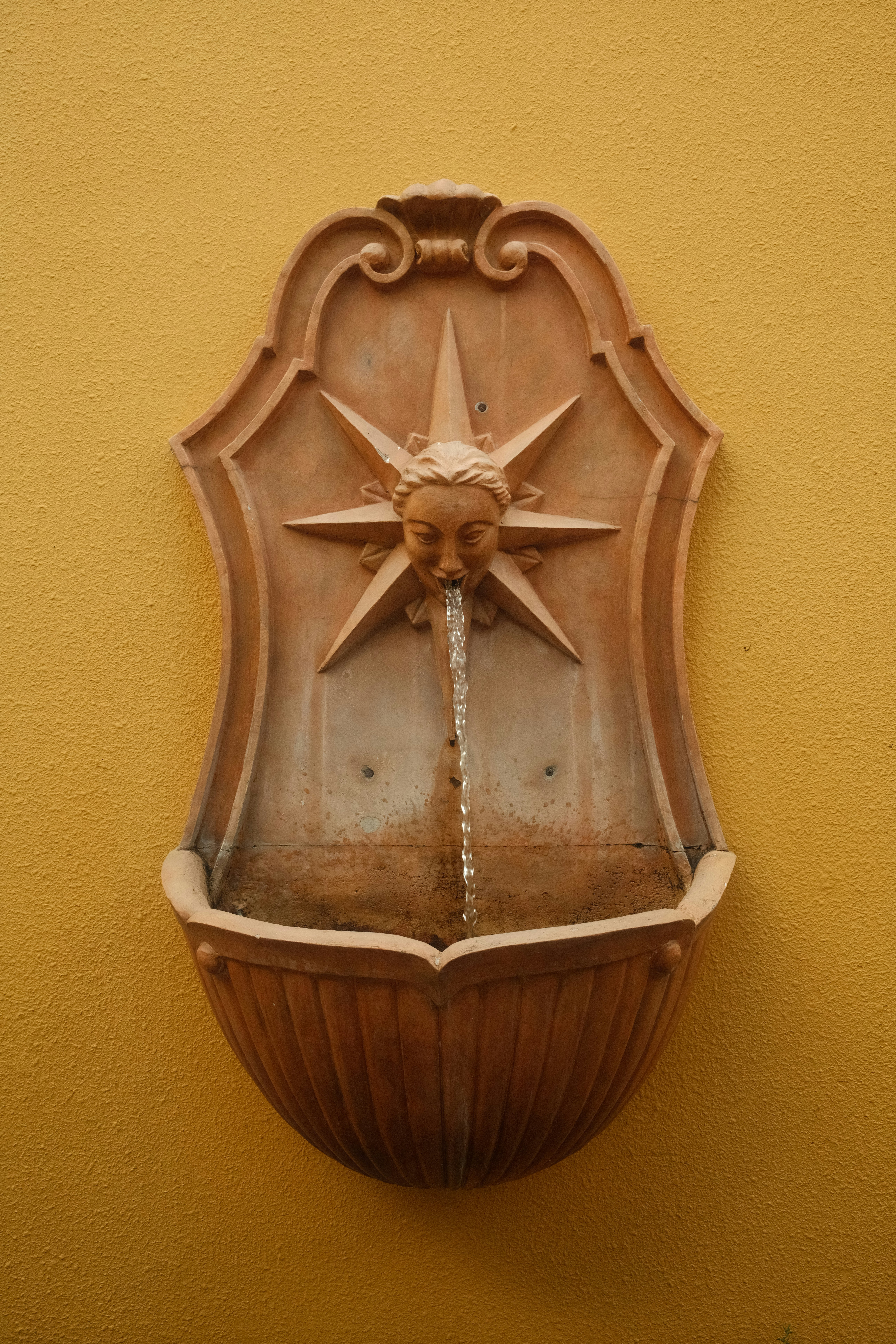 Sunlit Spout: A Stone Star Fountain on Golden Wall