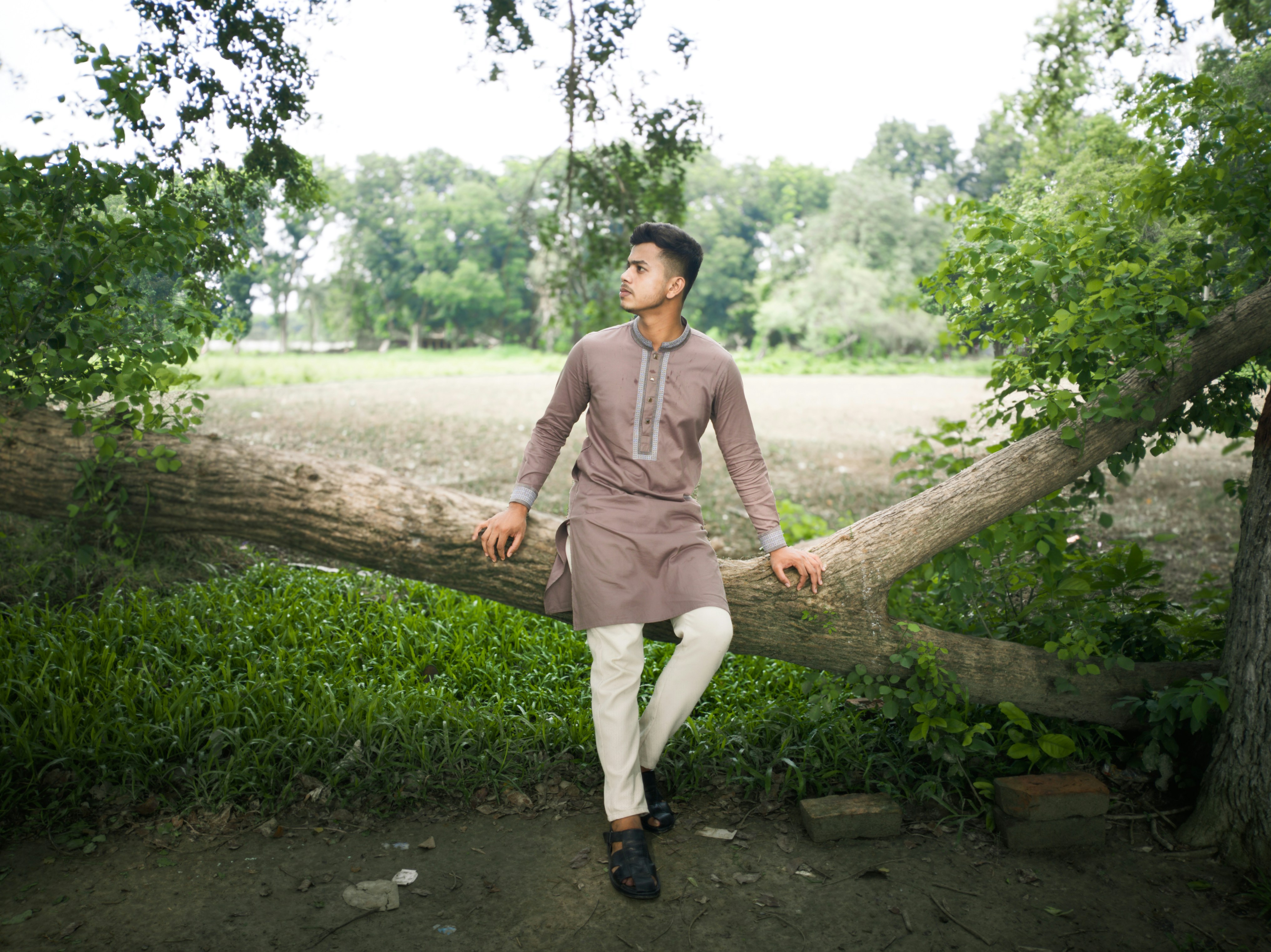 Man in traditional tunic perched on a fallen tree in a sunlit park
