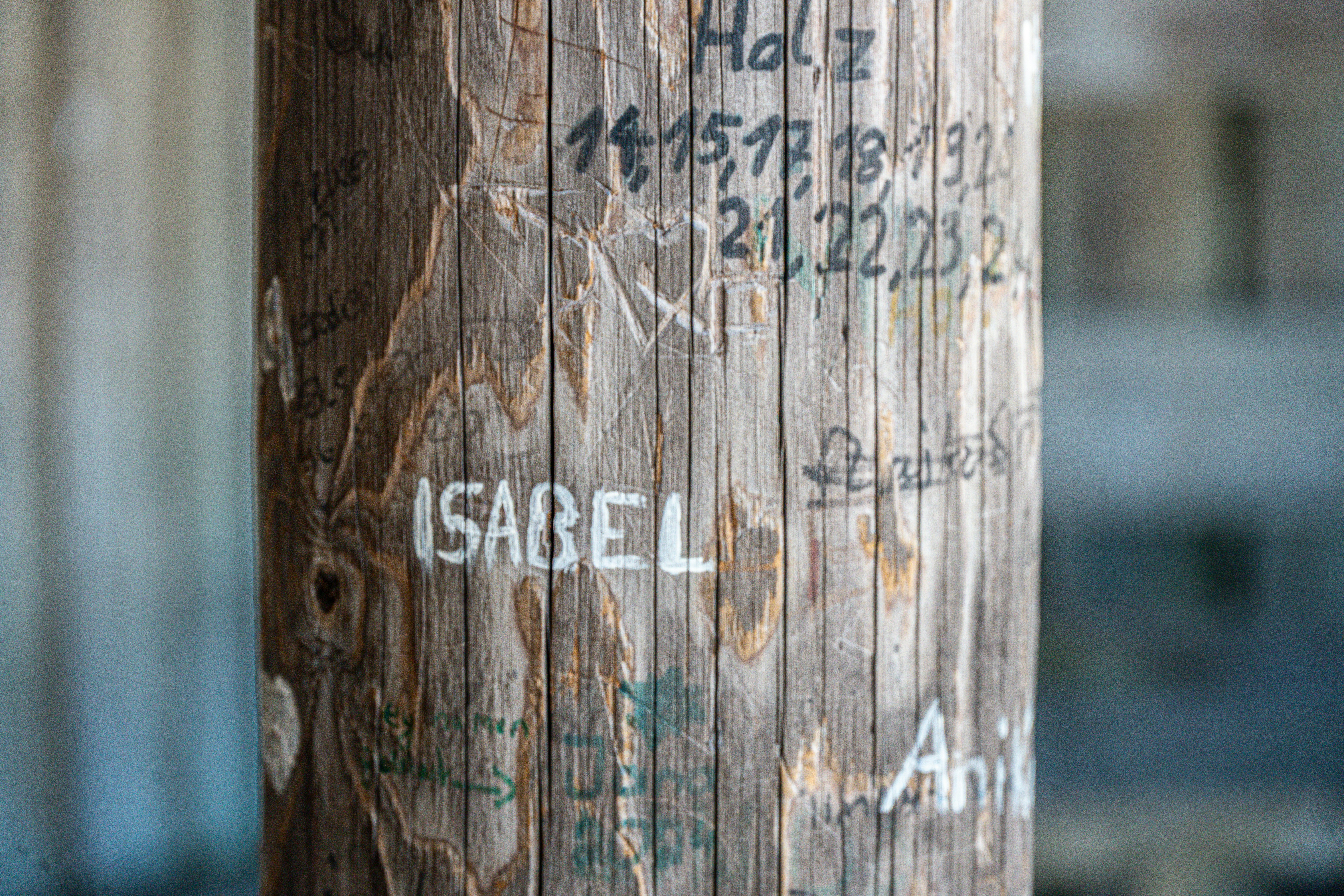 Weathered Graffiti on a Wooden Post: Names and Scribbles Etched in Time