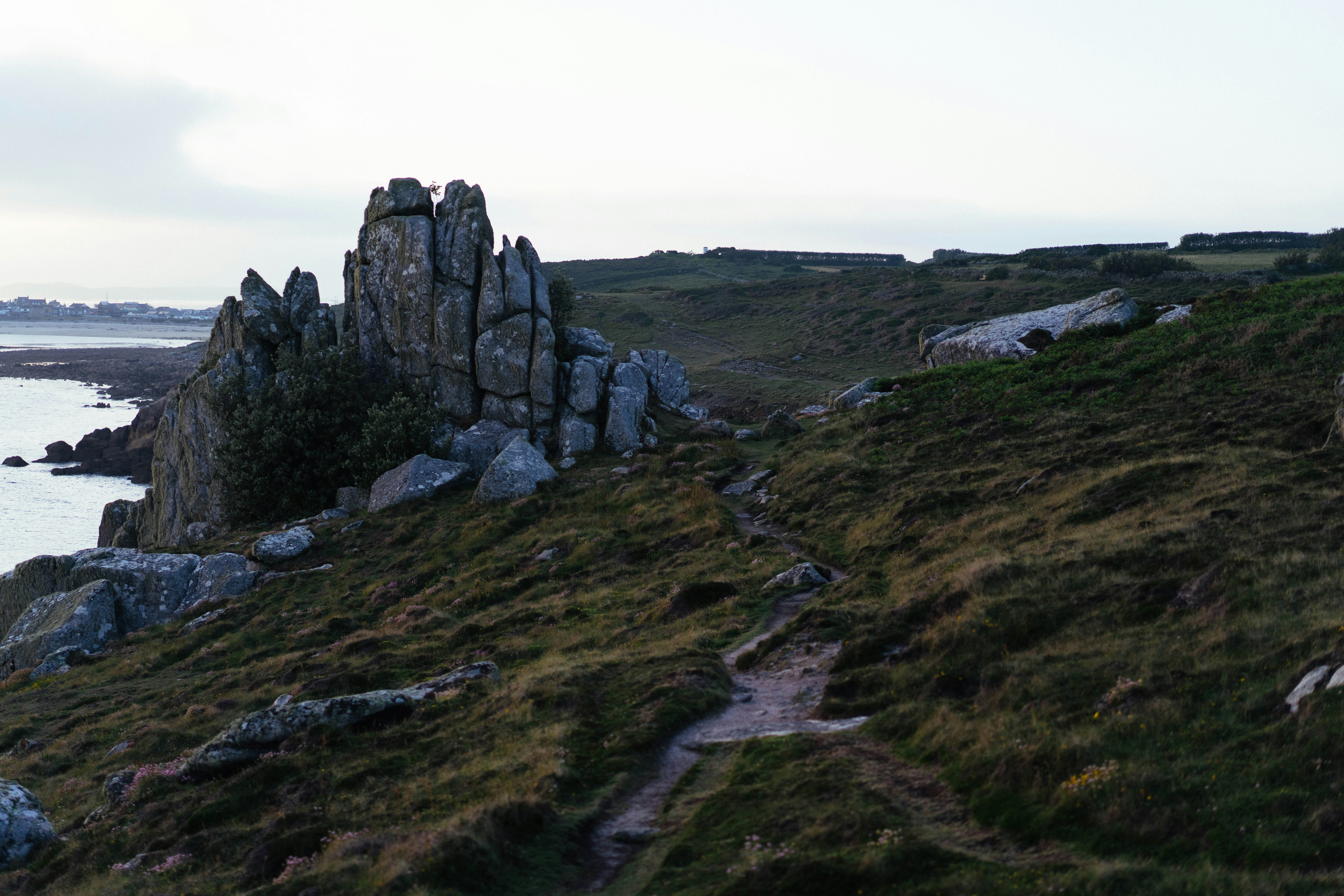 Rugged coastal path toward weathered rock sentinels under a spacious sky