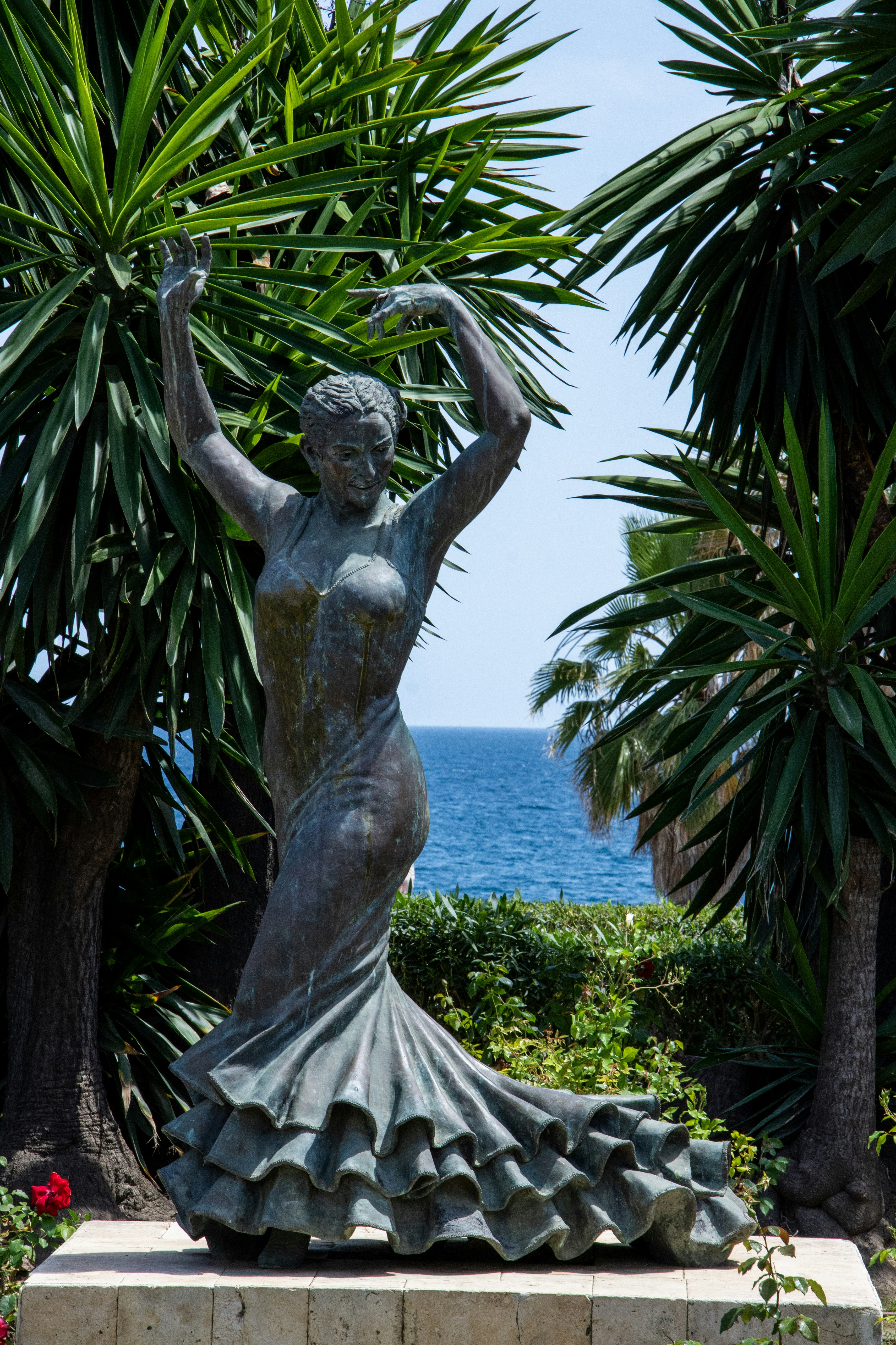 Statue in a Tropical Garden Framed by Spiky Palms with Sea View