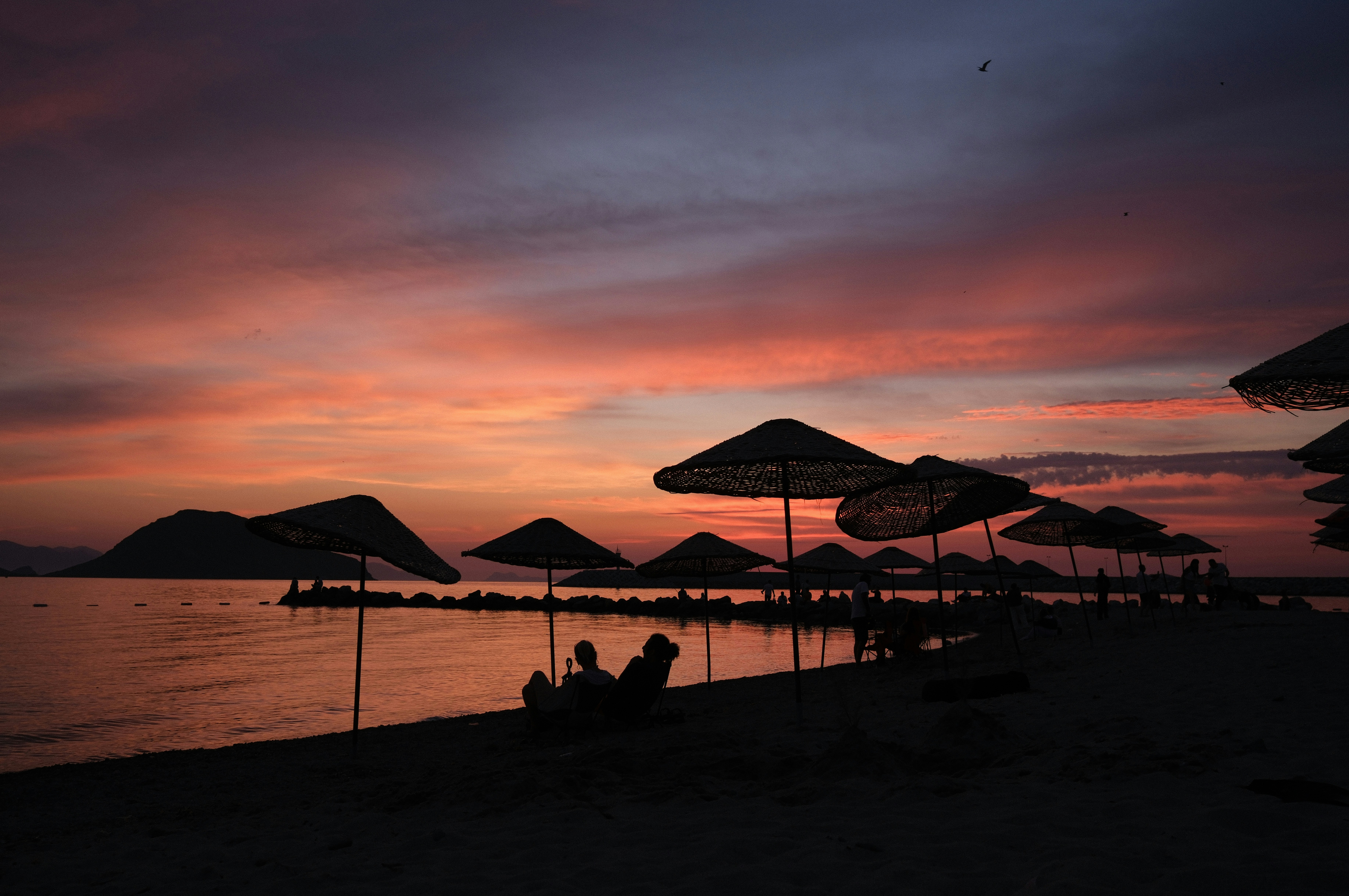 Silhouetted beach umbrellas and people against a vibrant sunset.