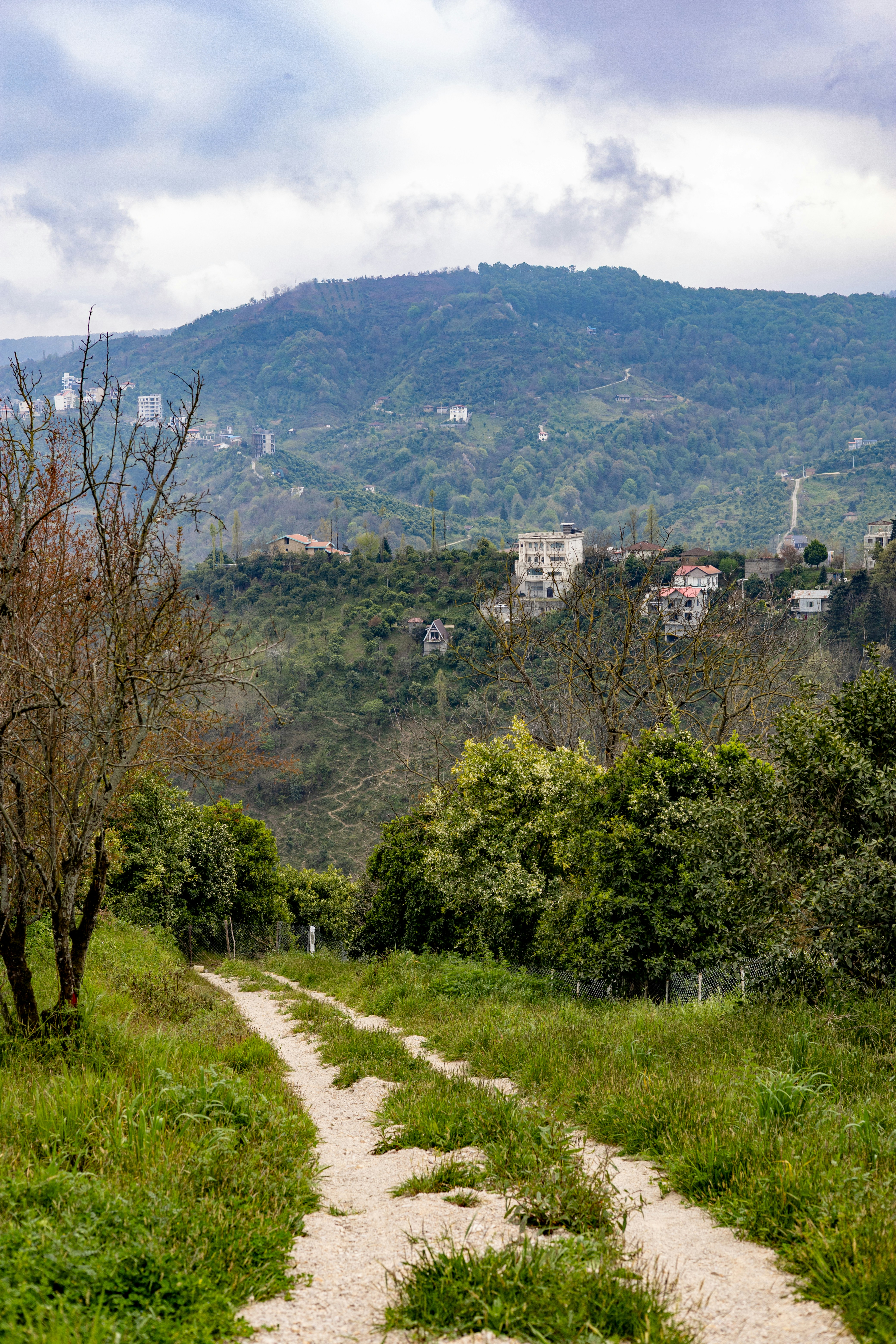 A dirt path descends through green hills with distant buildings.
