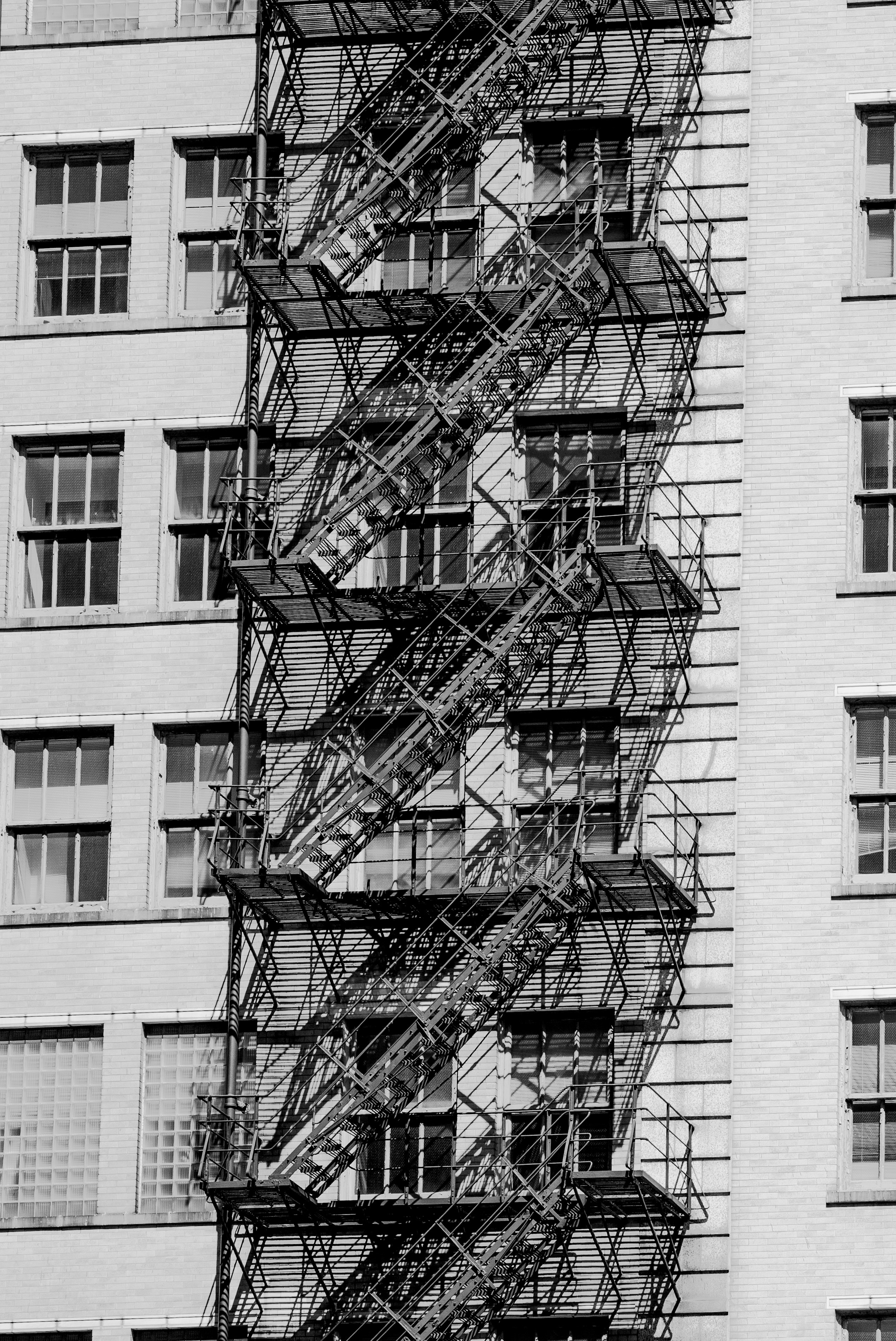 Vertical Lattice: Fire Escape Mesh on Sunlit Brick Facade