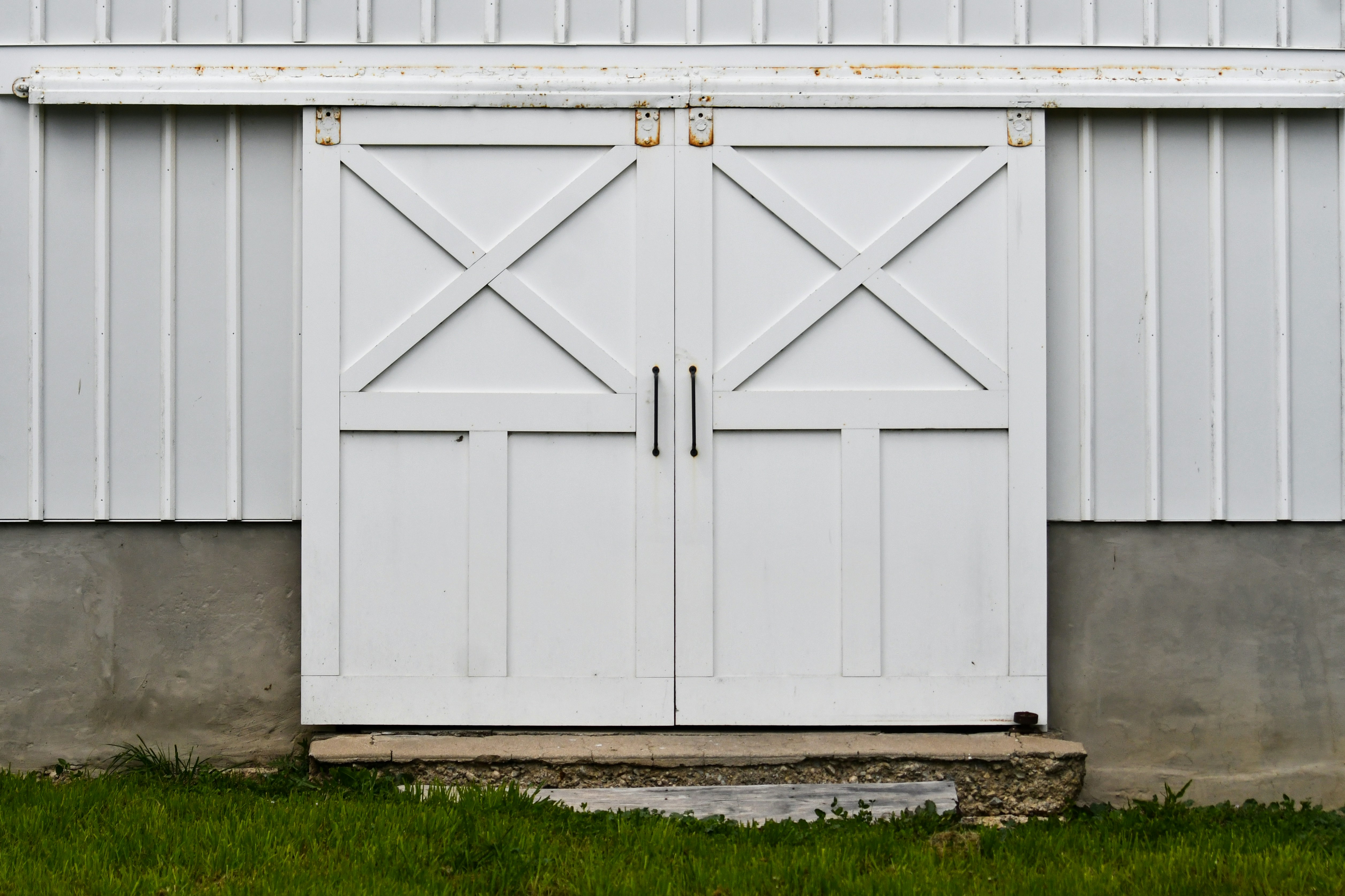 White barn doors framed by weathered gray siding and a chalky concrete threshold