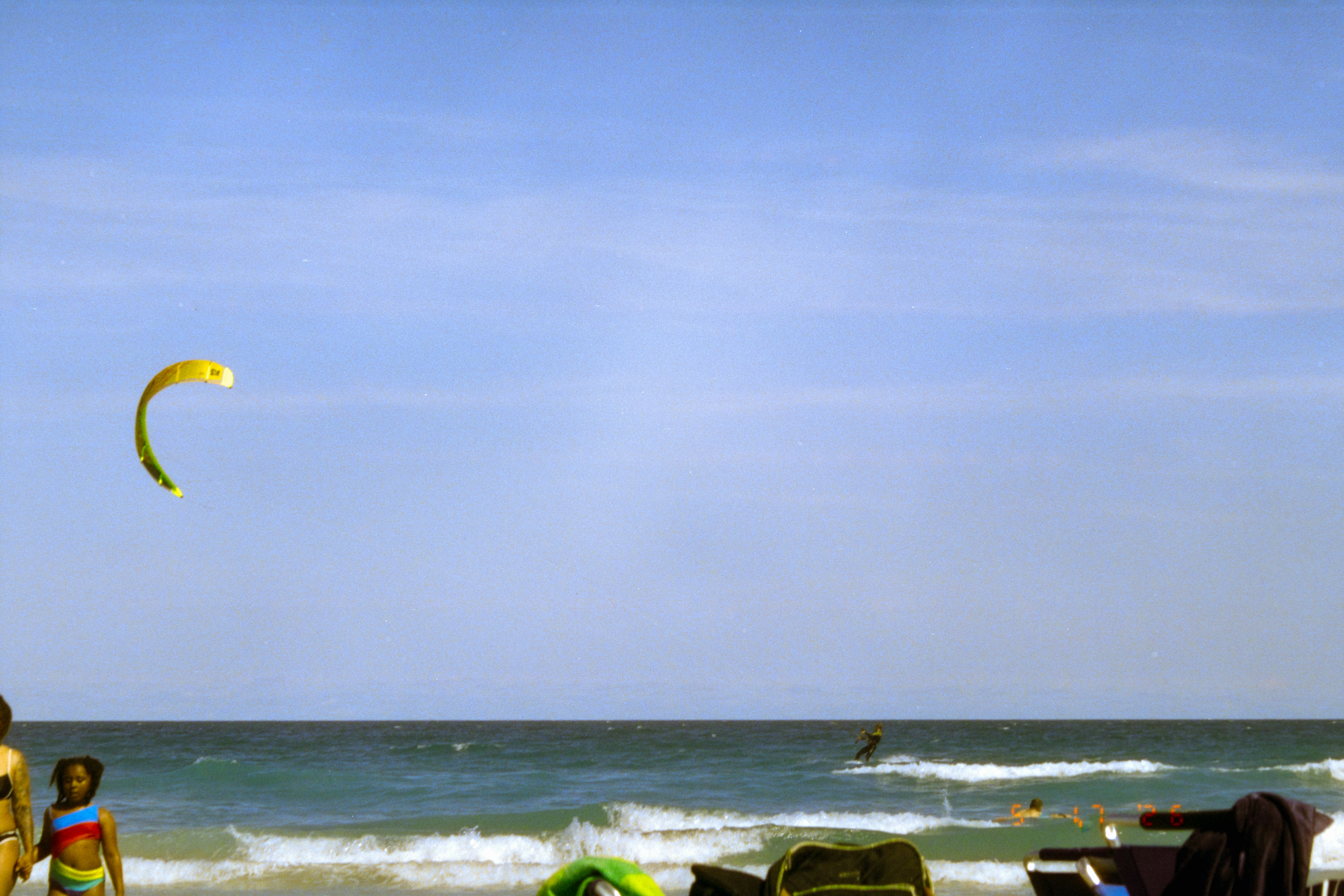 Kite gliding above a sunlit sea on a lively family beach