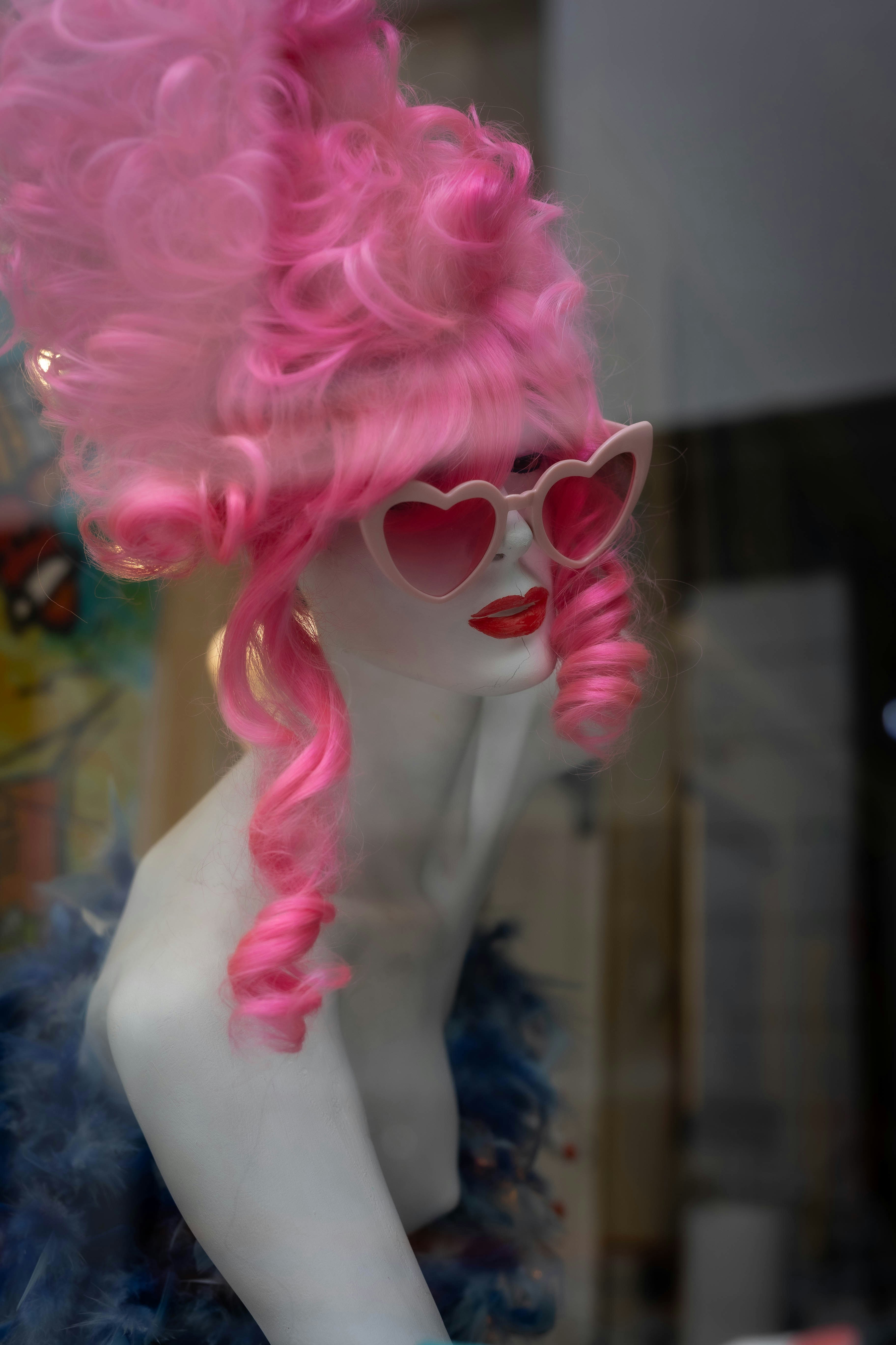 Pink-haired mannequin in heart-shaped sunglasses gleams in storefront glow