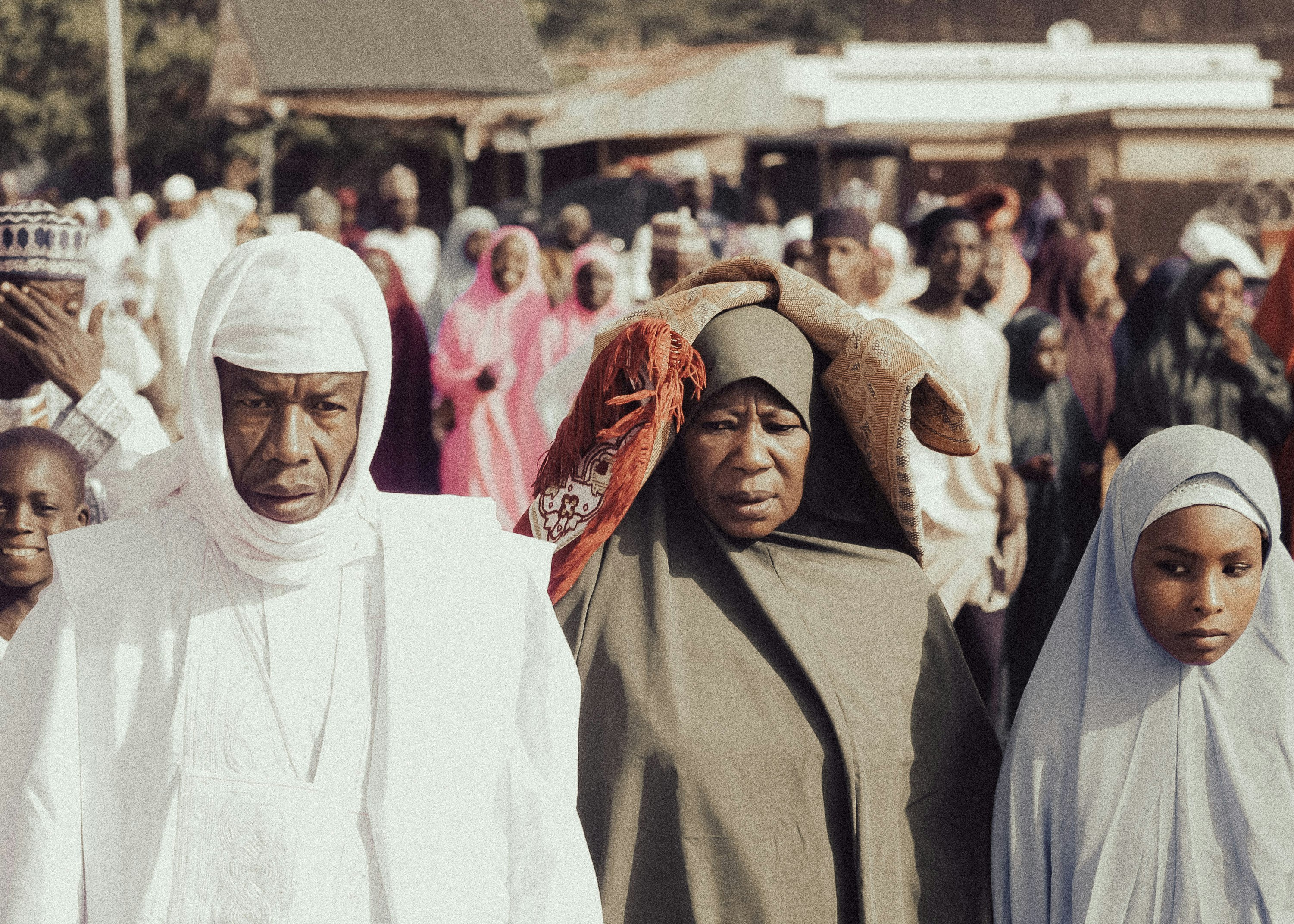 Center of Quiet Resolve: A trio in White, Brown, and Blue Abayas Amid a Bustling Market Crowd