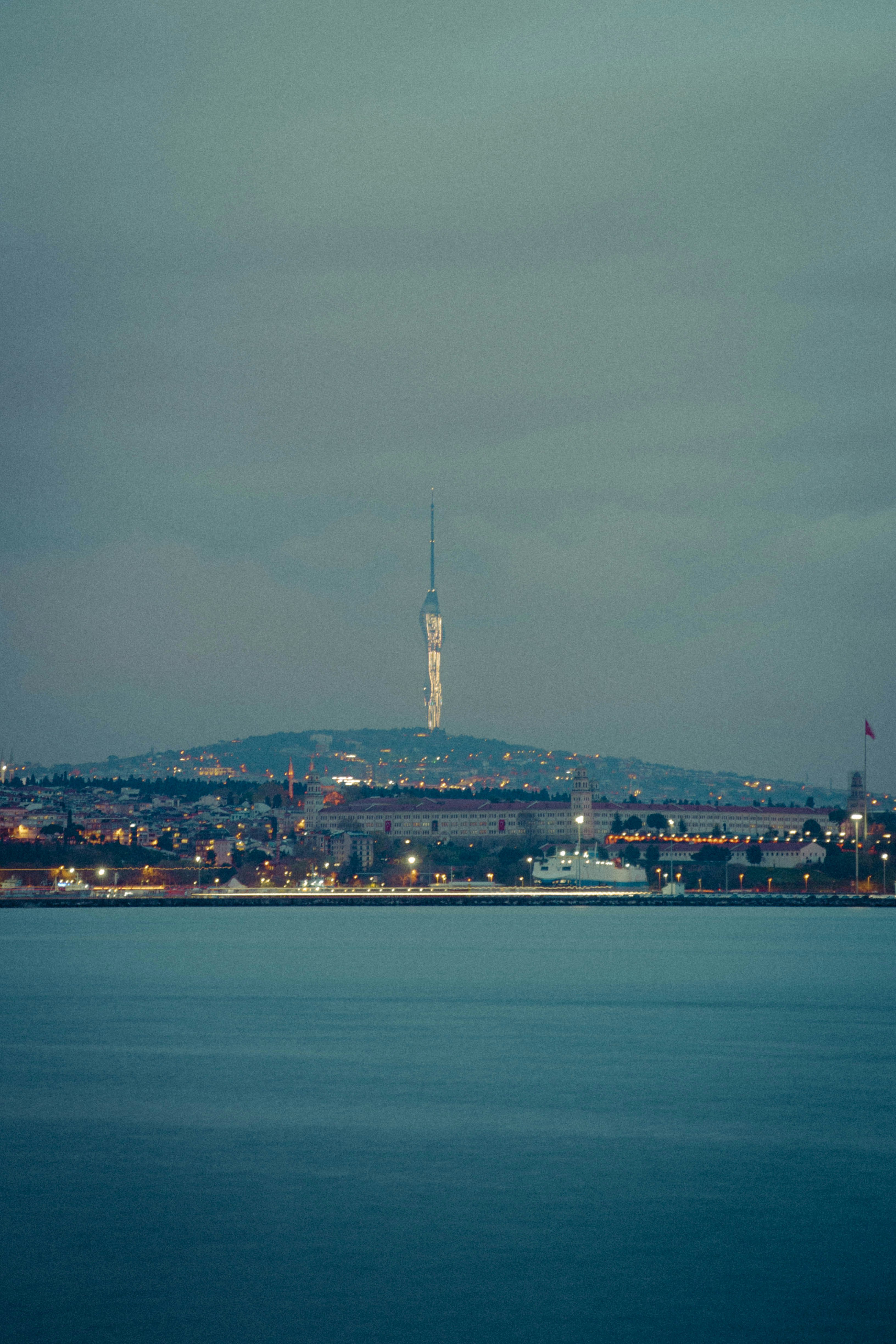 Tall Needle Over Peninsula: City Lights Beneath a Calm Harbor