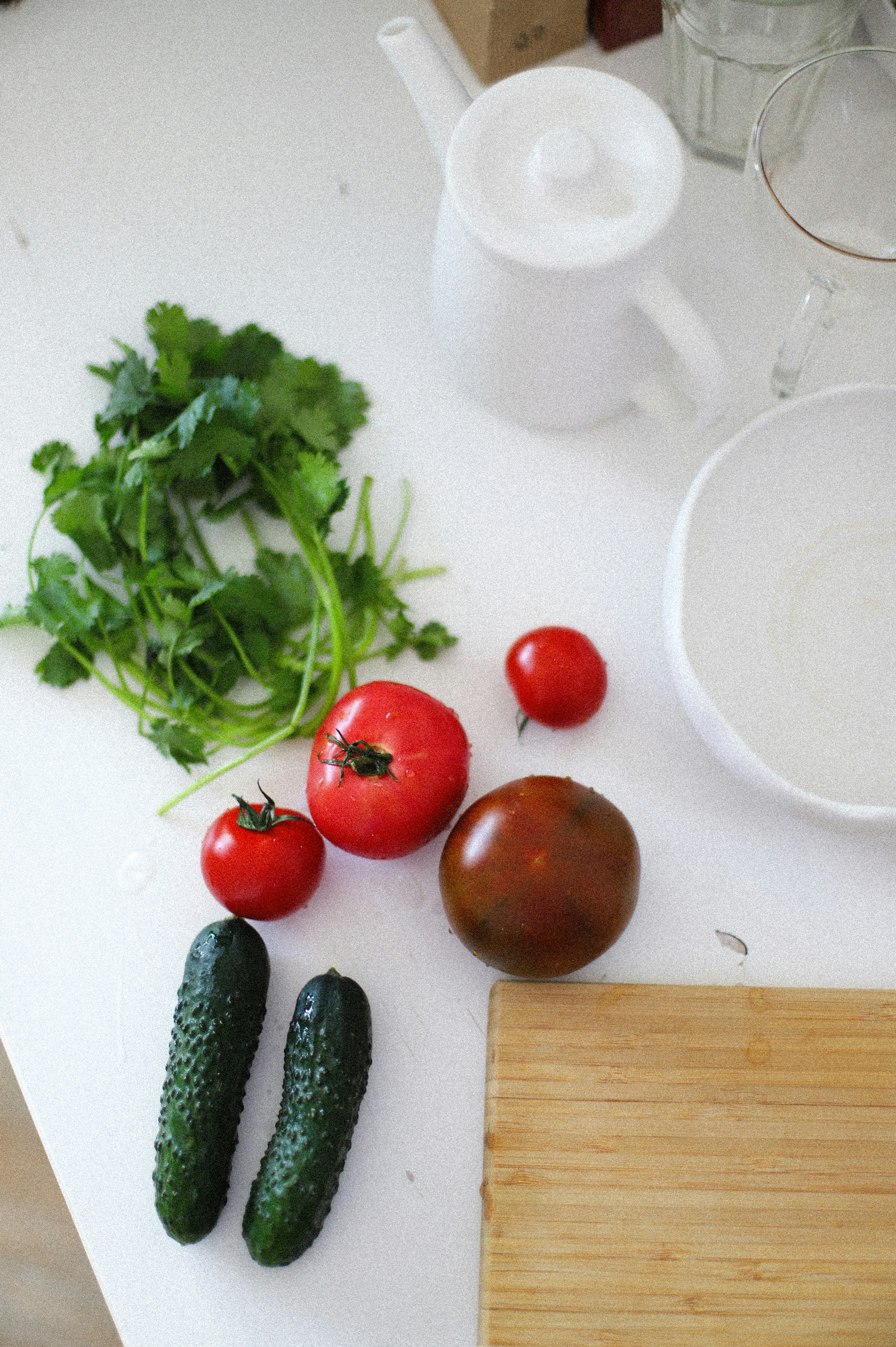 Scatter of fresh harvest: tomatoes, cucumbers, and herbs on a white prep surface