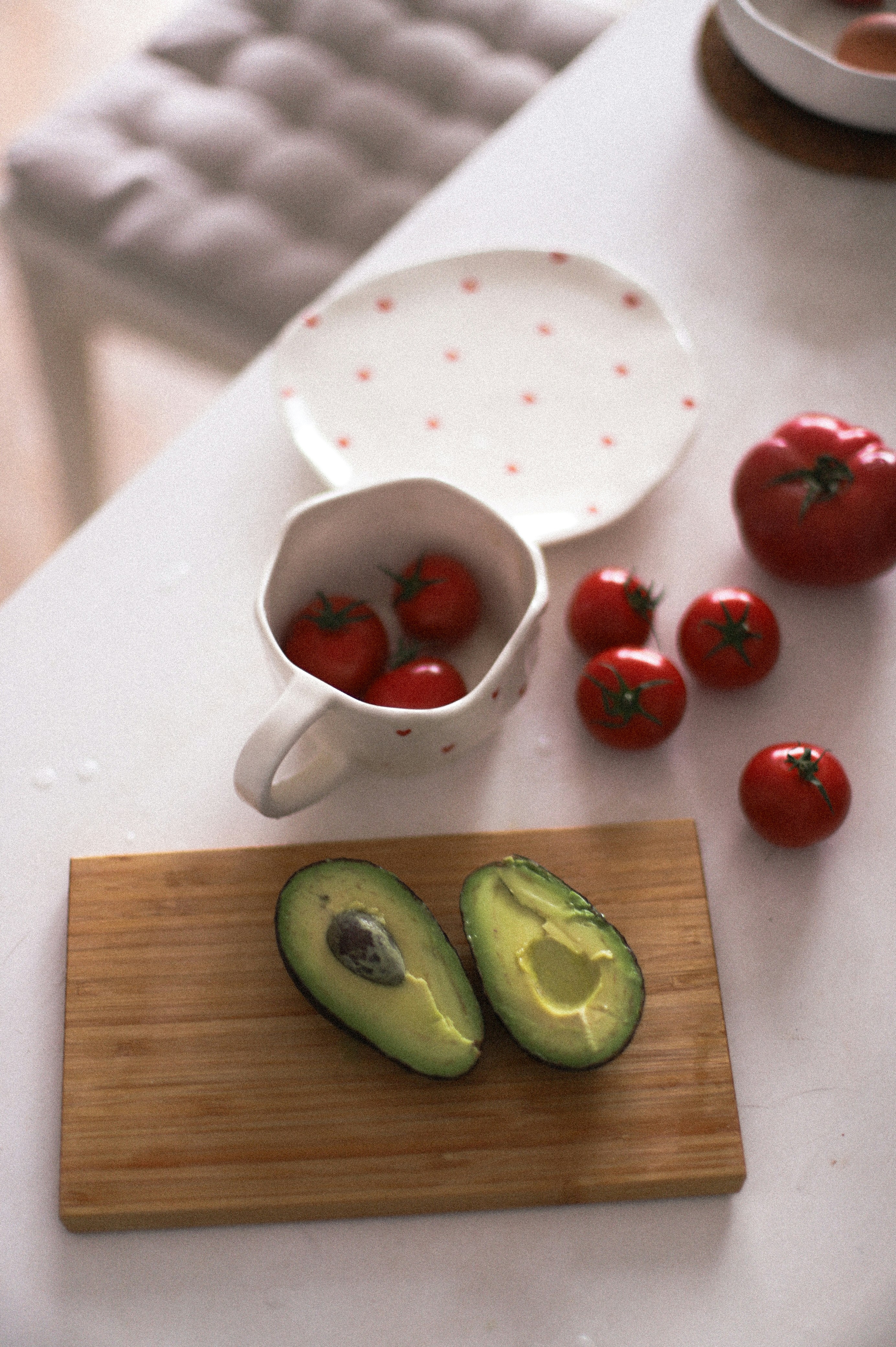 Half-cut avocado on wooden board with pearly tiles and cherry tomatoes on a white countertop