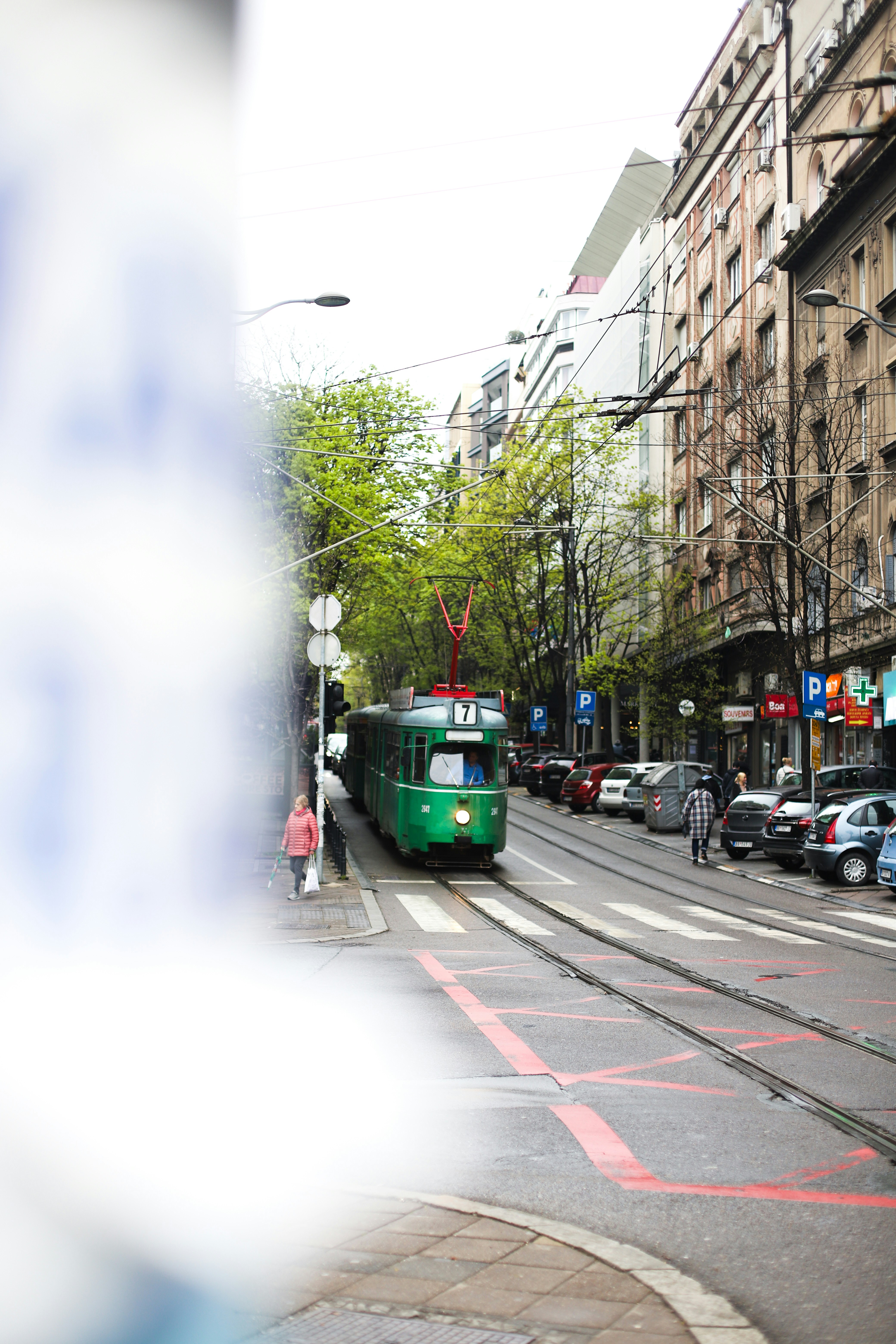 Green Tram on a City Street, Framed by Passing Traffic and Historic Buildings