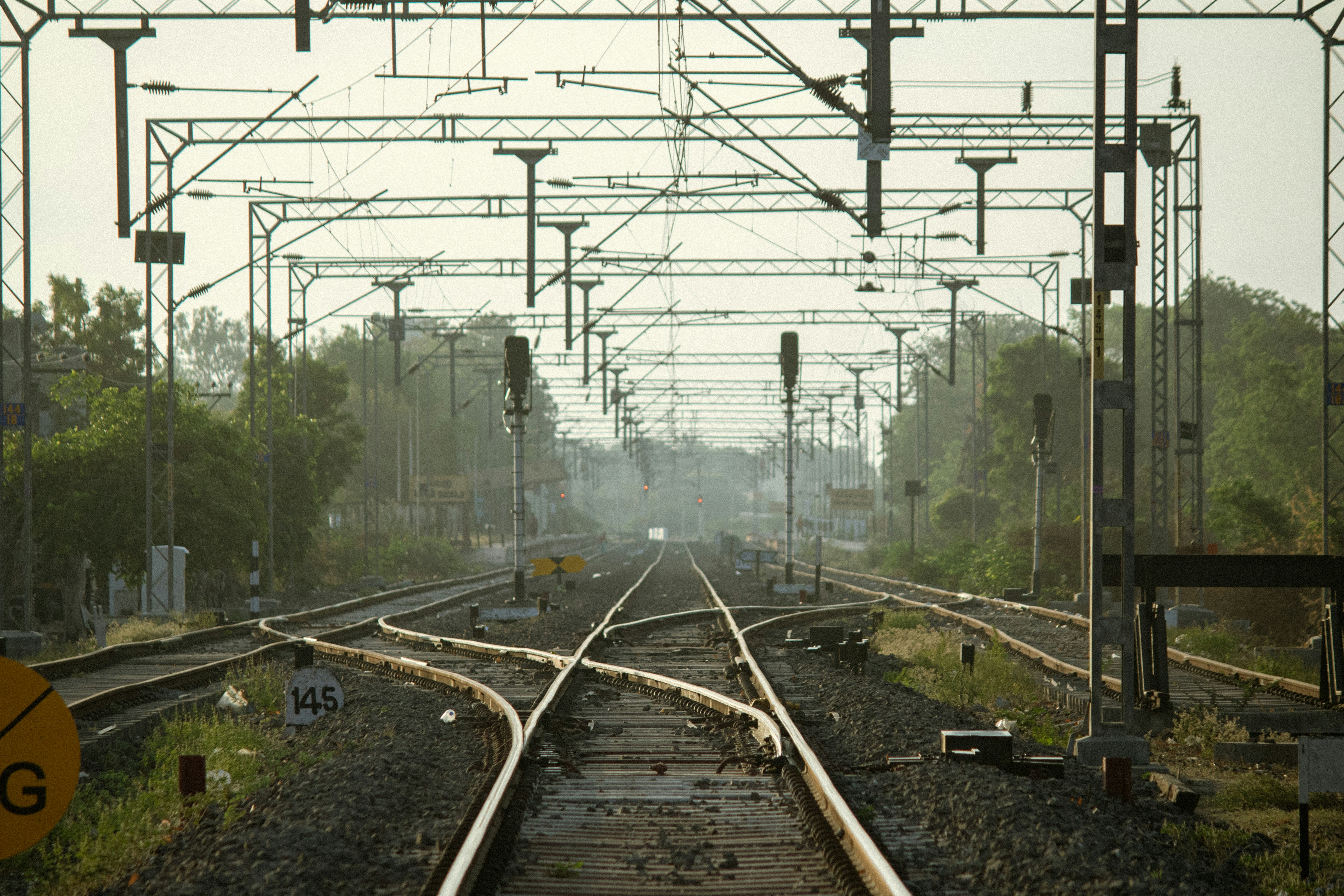Two converging railway tracks stretch toward the horizon beneath an overhead catenary structure, creating a sense of depth and perspective.