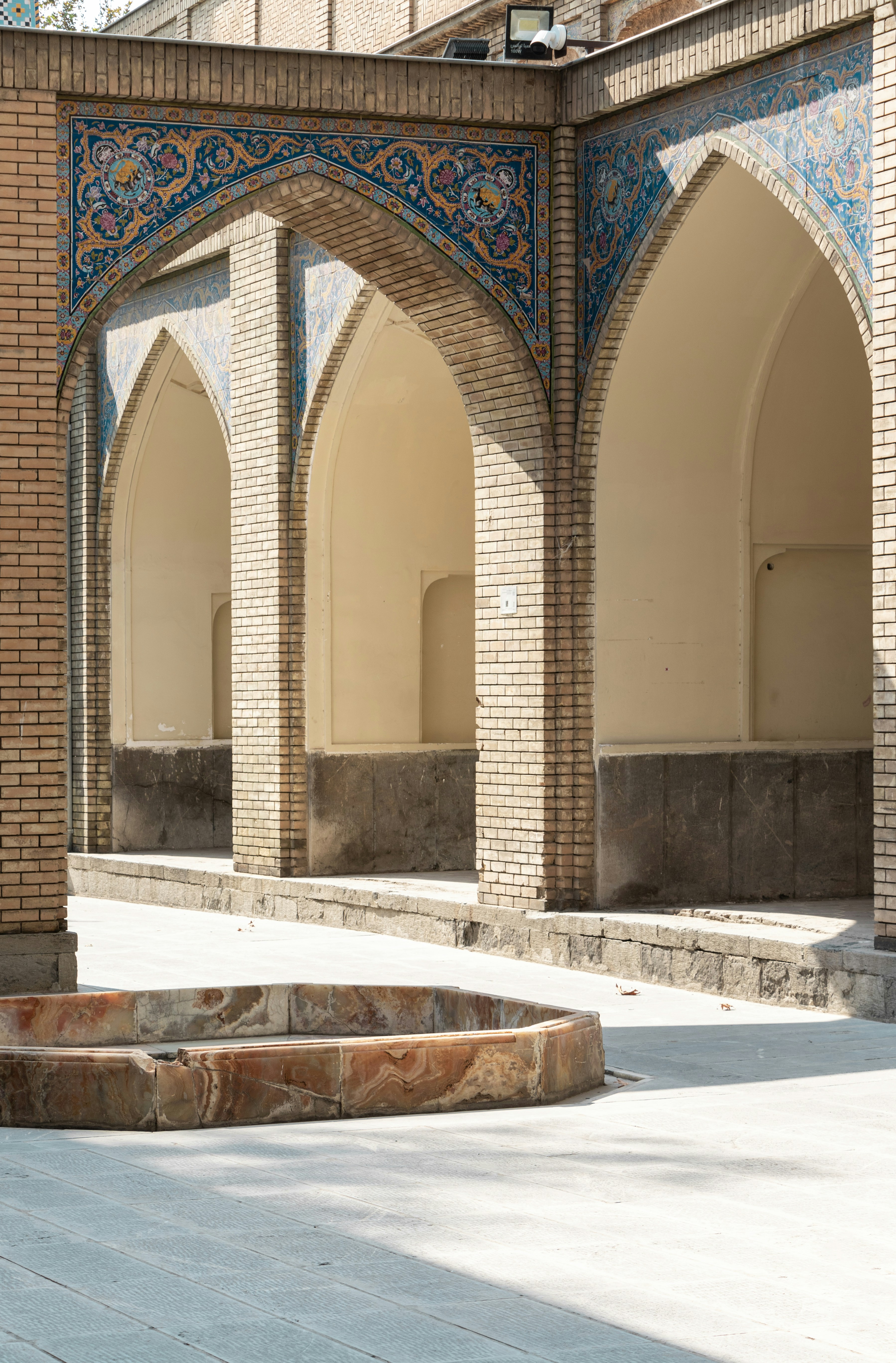 Arched Courtyard Walkway: Sunlit Brickwork and Ornate Tile Frieze