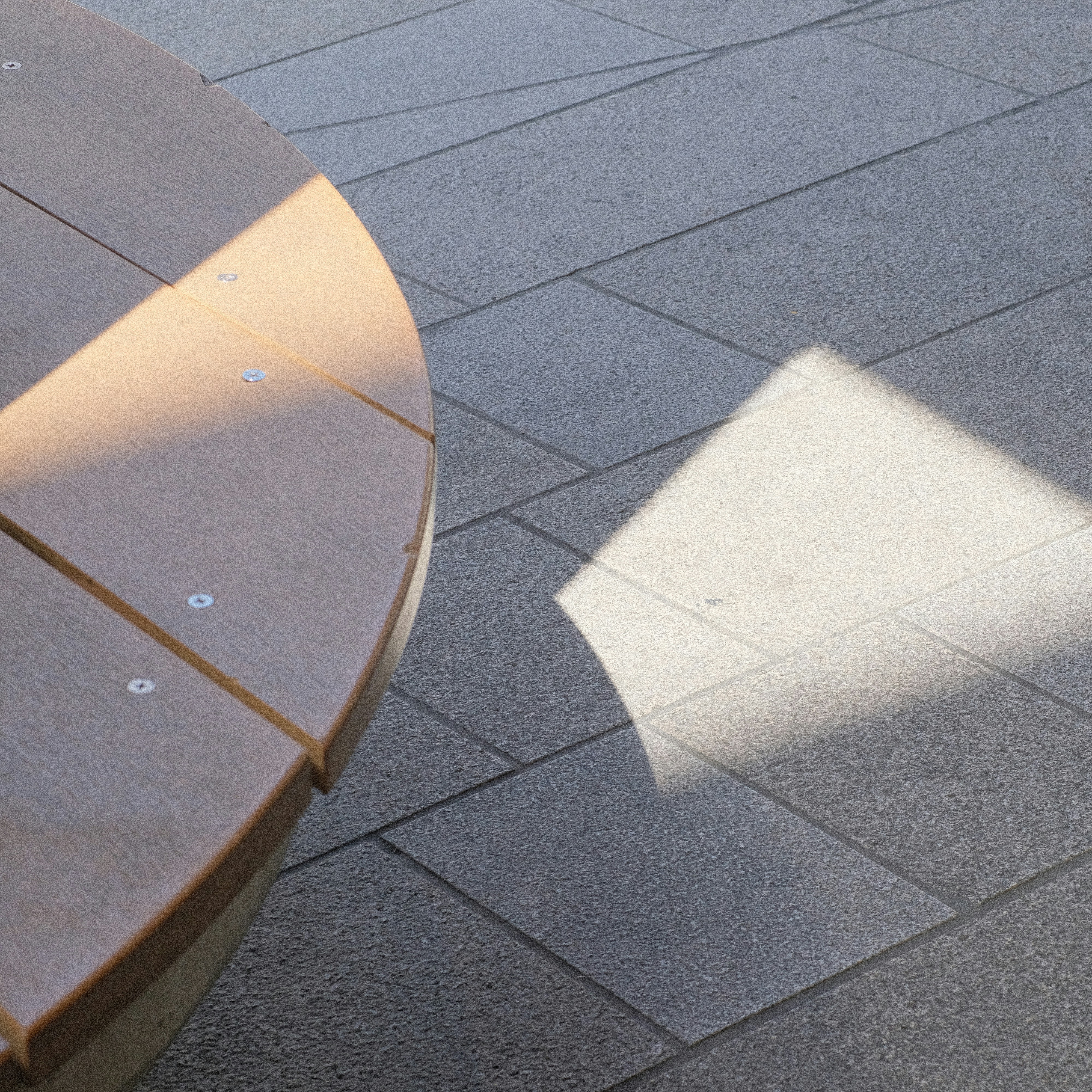 Curved wooden bench meets sunlit geometry