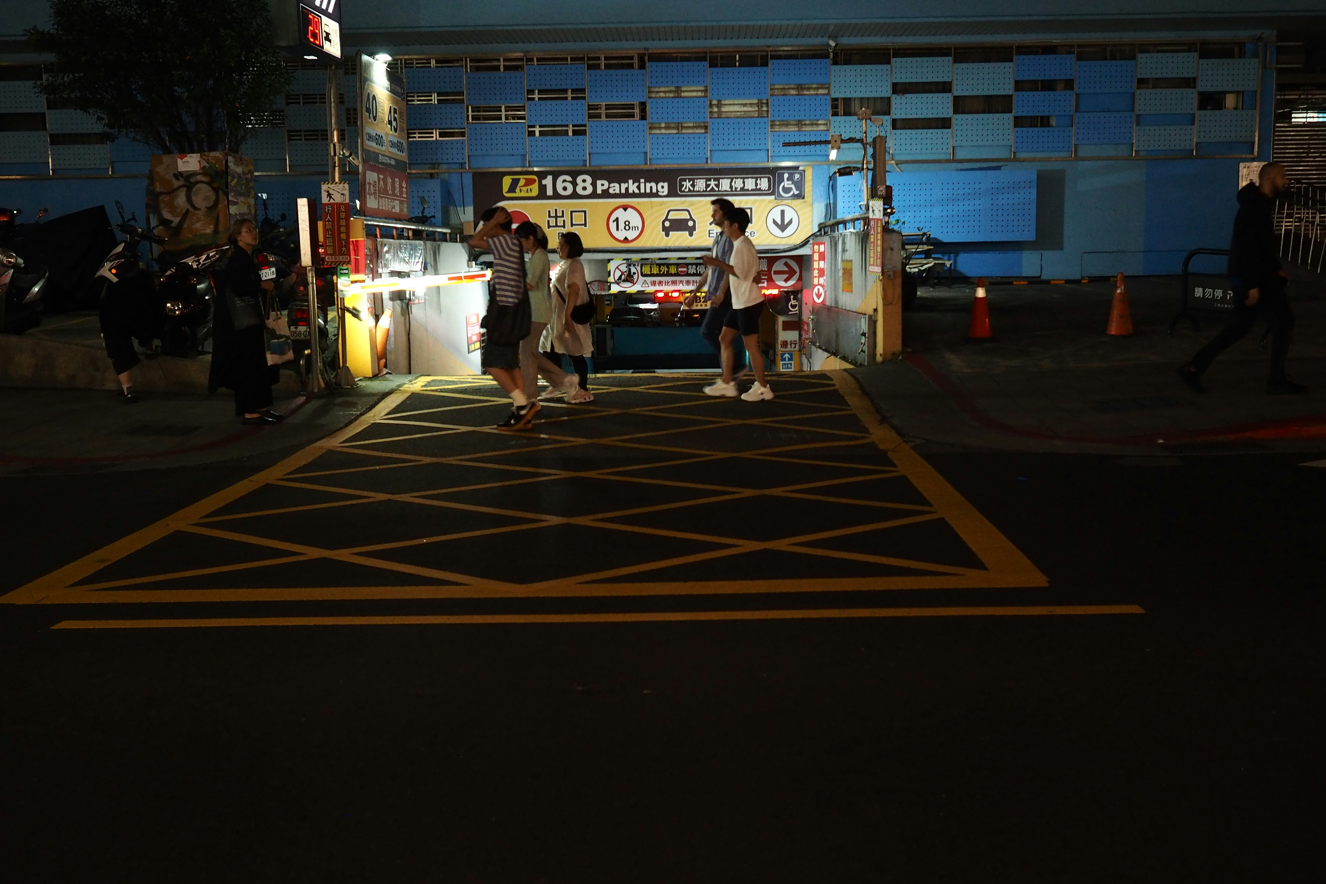 Night Gate: People Entering a Parking Assembly Through a Neon-Outlined Barrier