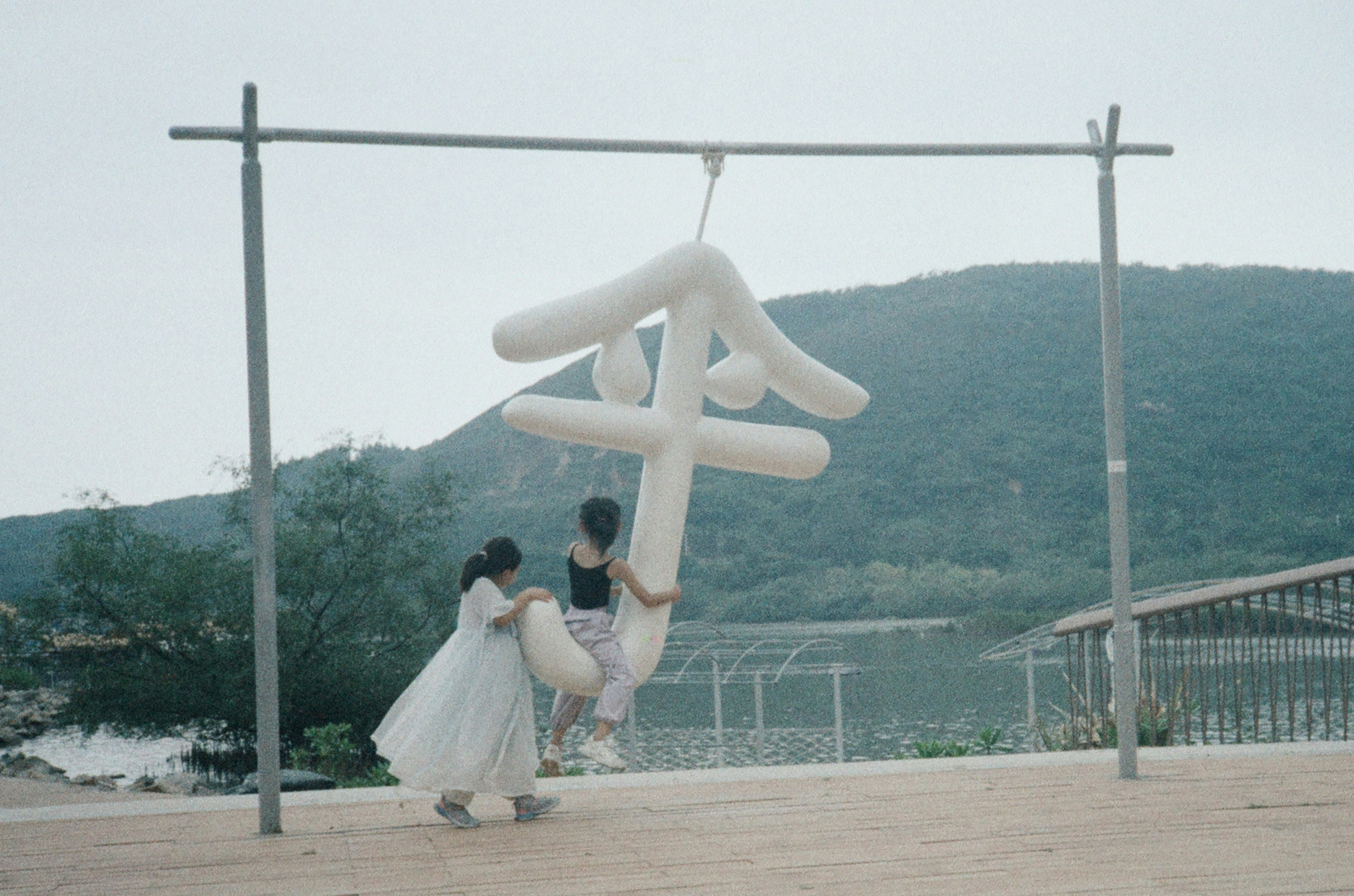 Three figures and a whimsical swing sculpture by the lake