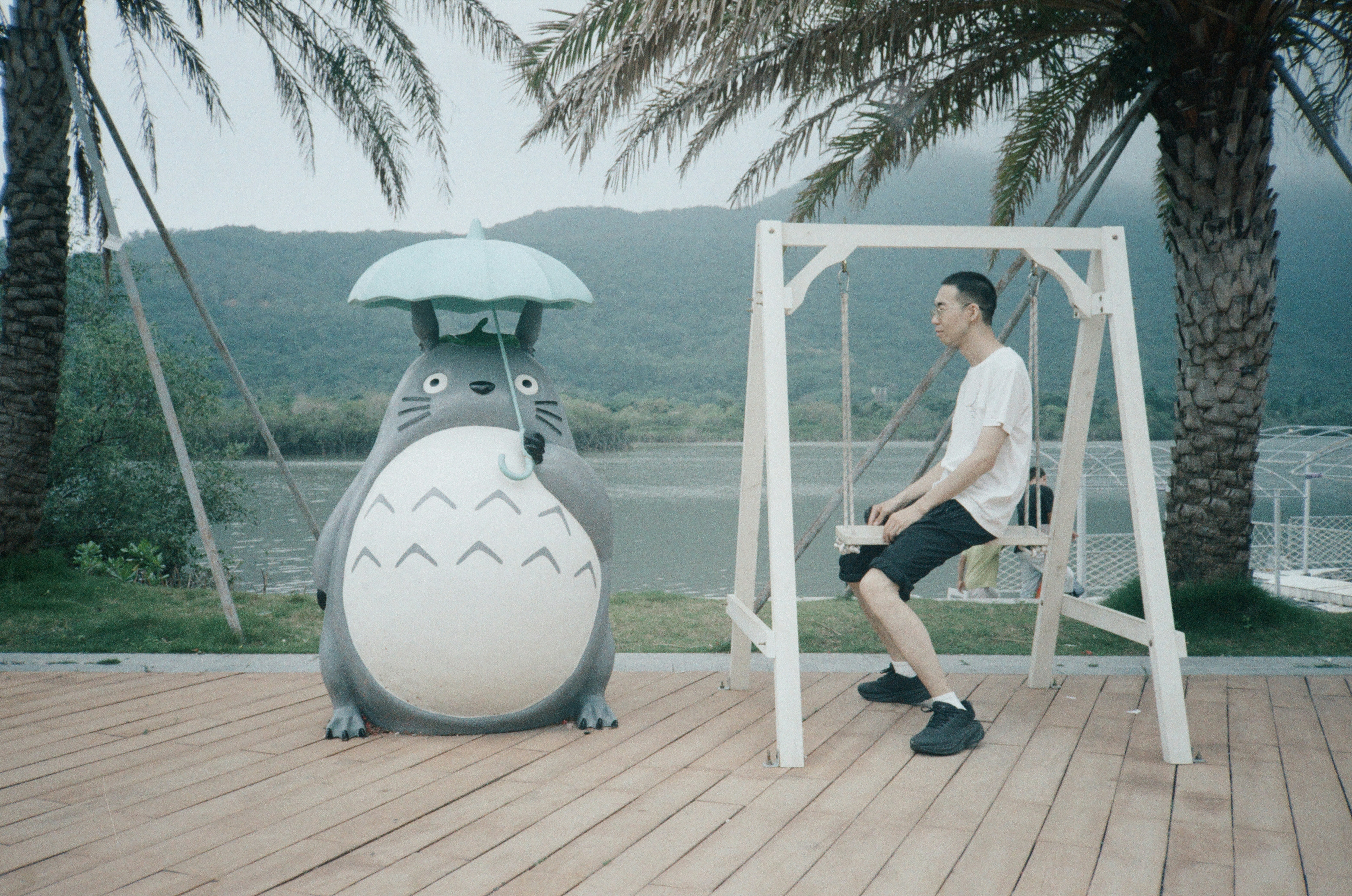 Sunlit Pause: Man on a Swing Beside a Totoro Statue