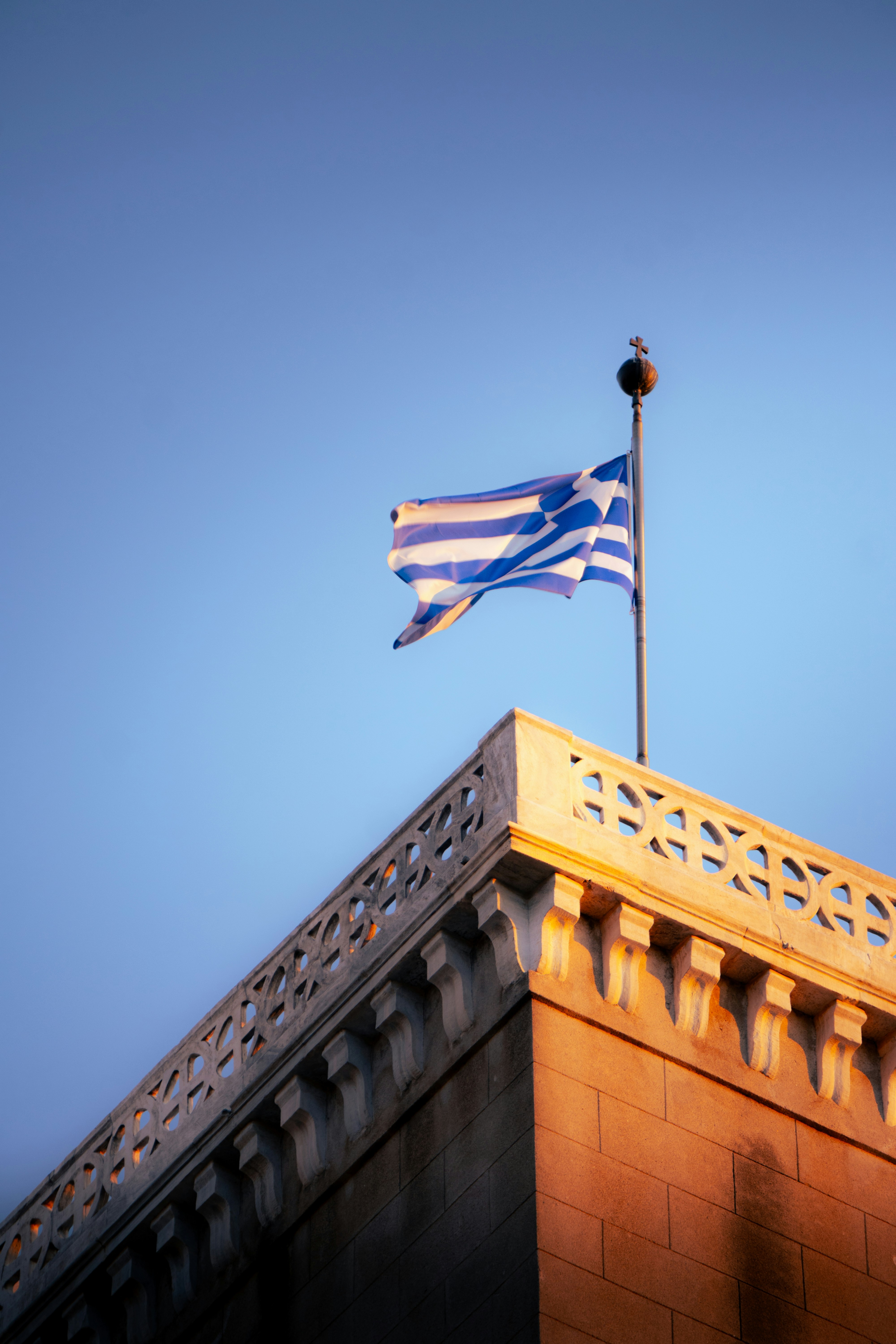 Flag atop sunlit terrace: a Greek-inspired silhouette against a clear sky