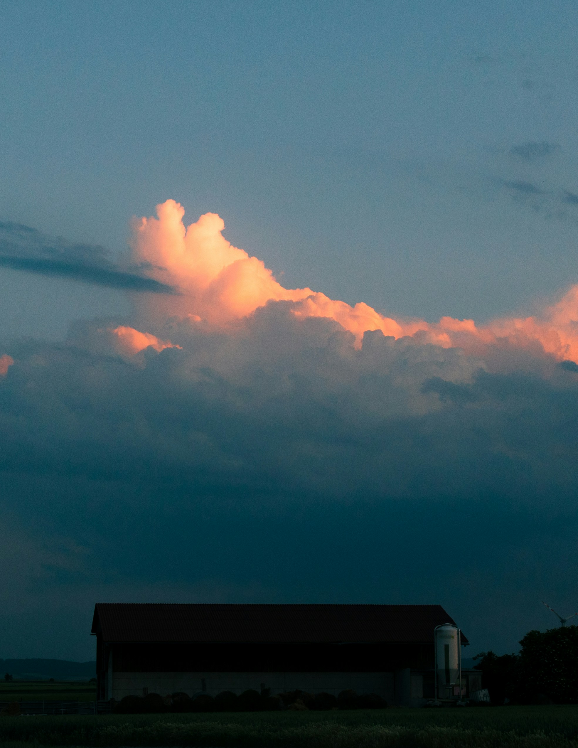 Cloud-loom over a quiet barn under a dusk-tinged sky
