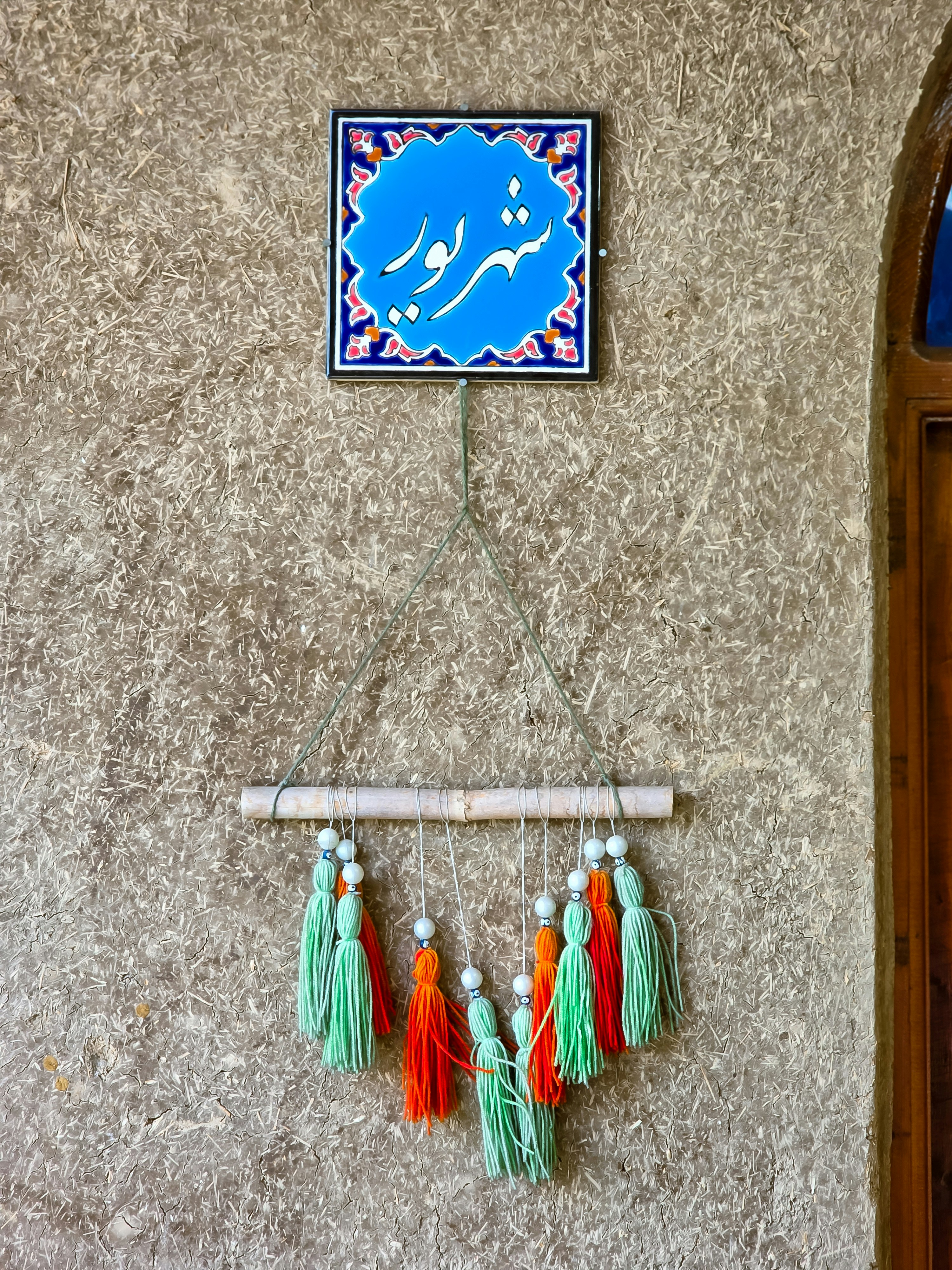 Hanging Textile Ornament Beneath a Ceremonial Plaque on a Rough Wall