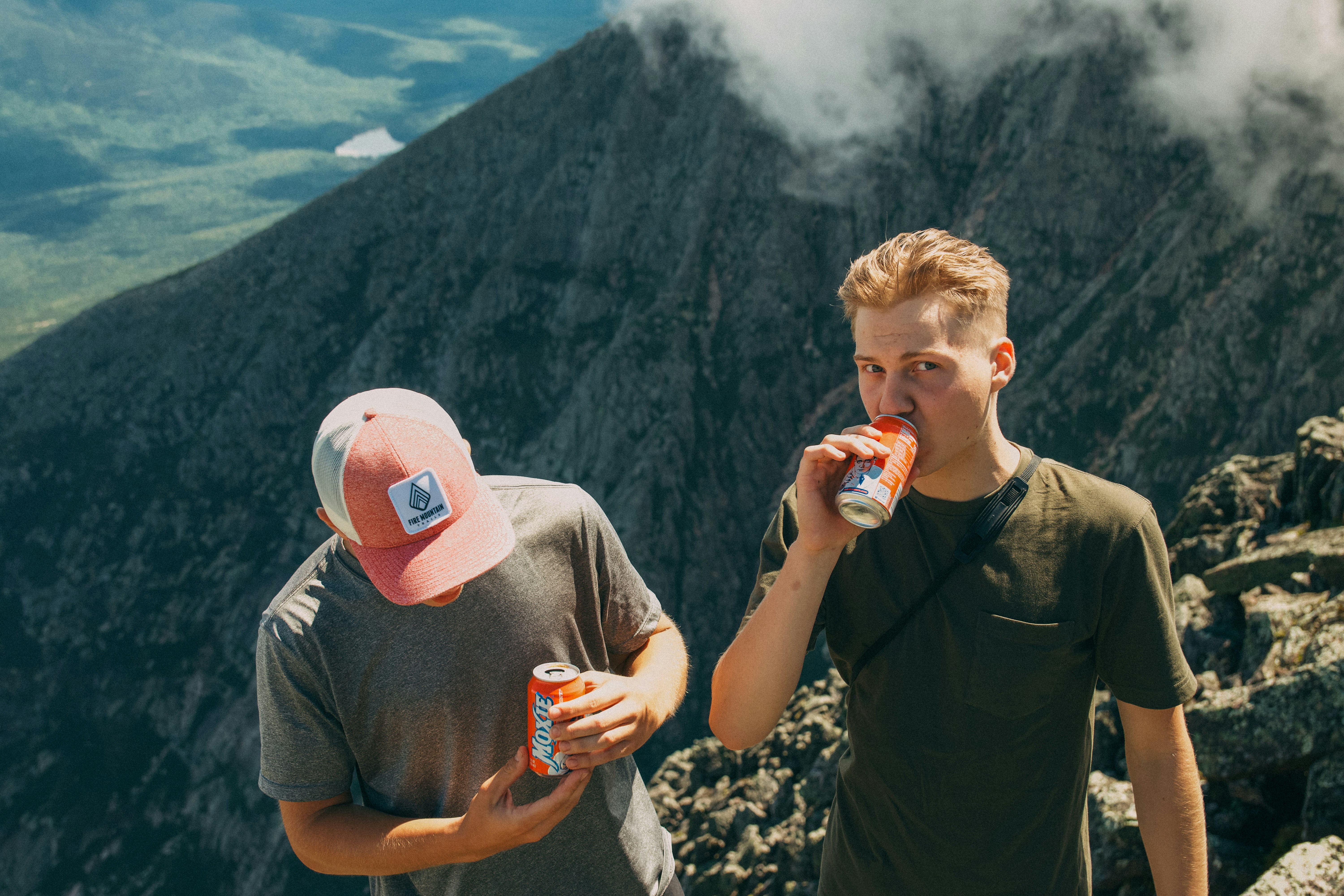 Summit Break: Two Friends Enjoy a Canned Refresh at the Edge of a Mountain Crag