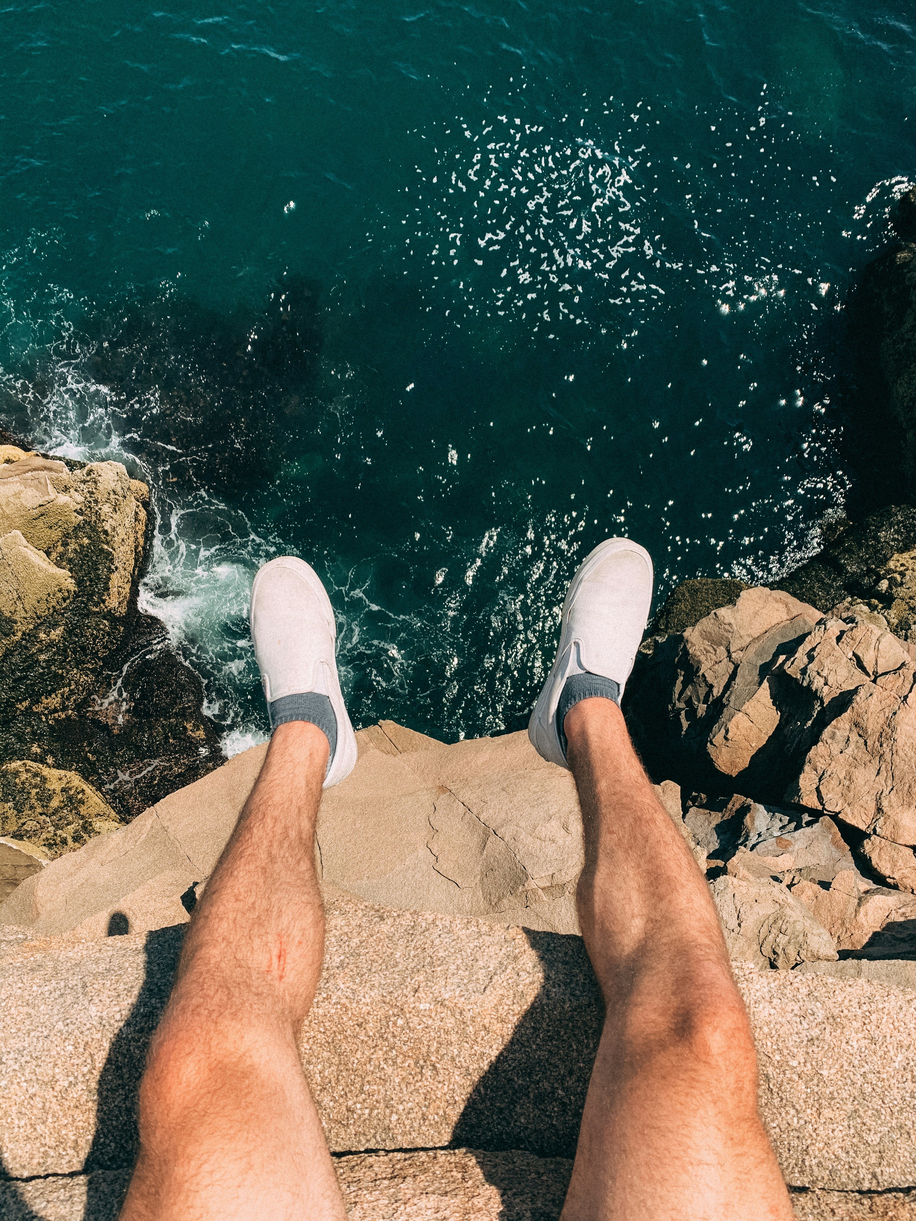 Daring cliffside view: legs swinging above turquoise surf