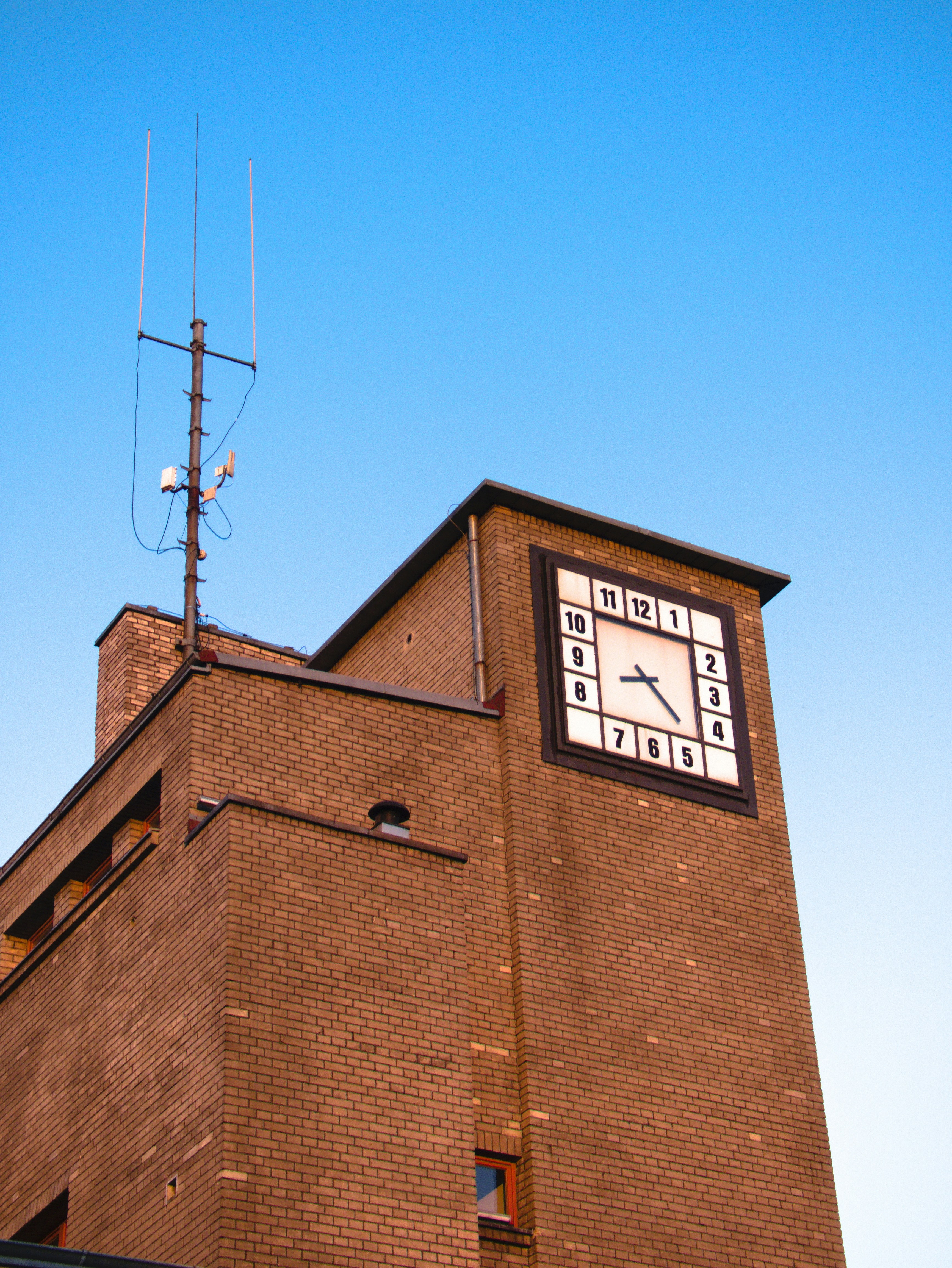 Brick Clock Tower with Antenna Under a Clear Blue Sky