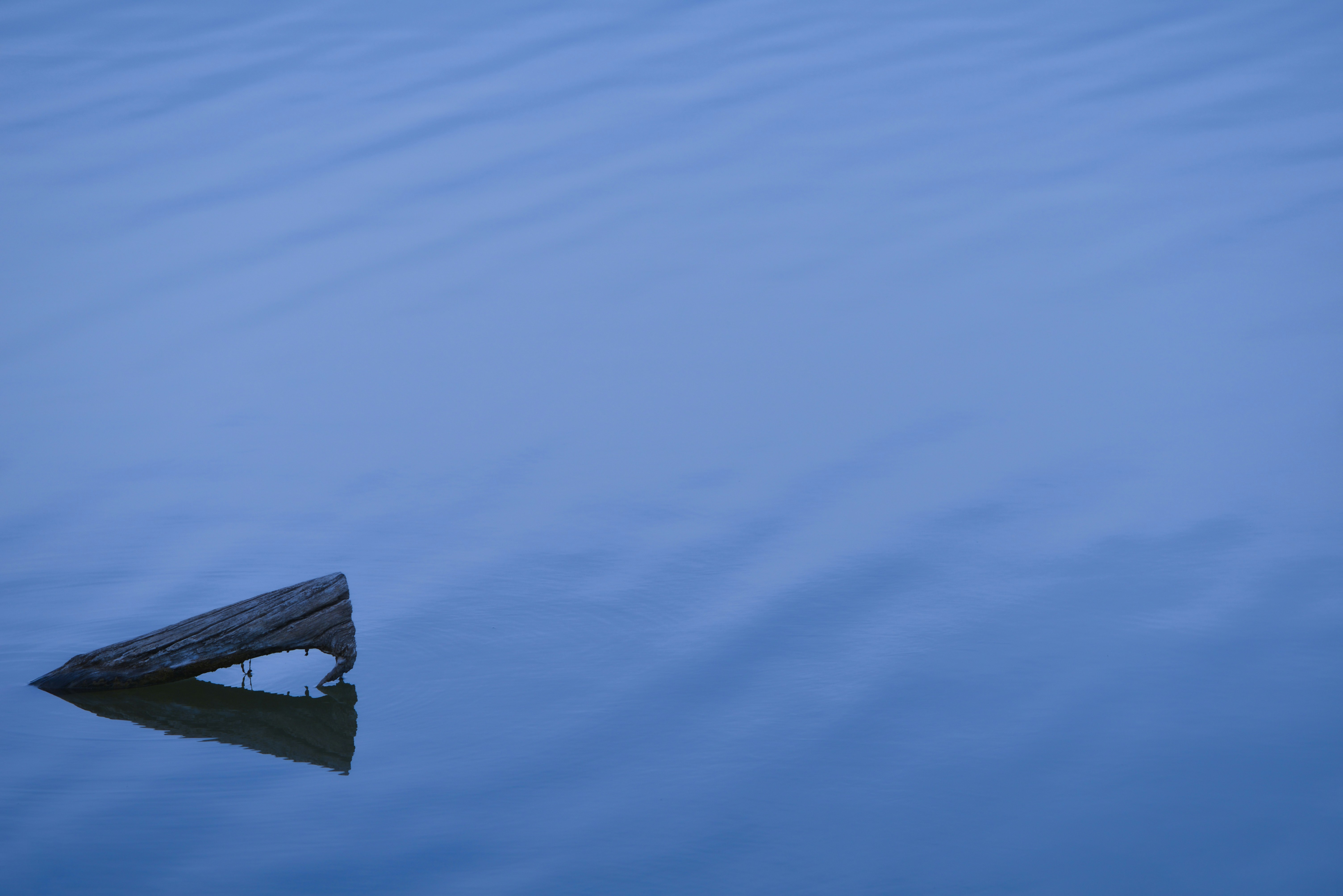 Solitary Drift: A Weathered Log Treading Quiet Waters