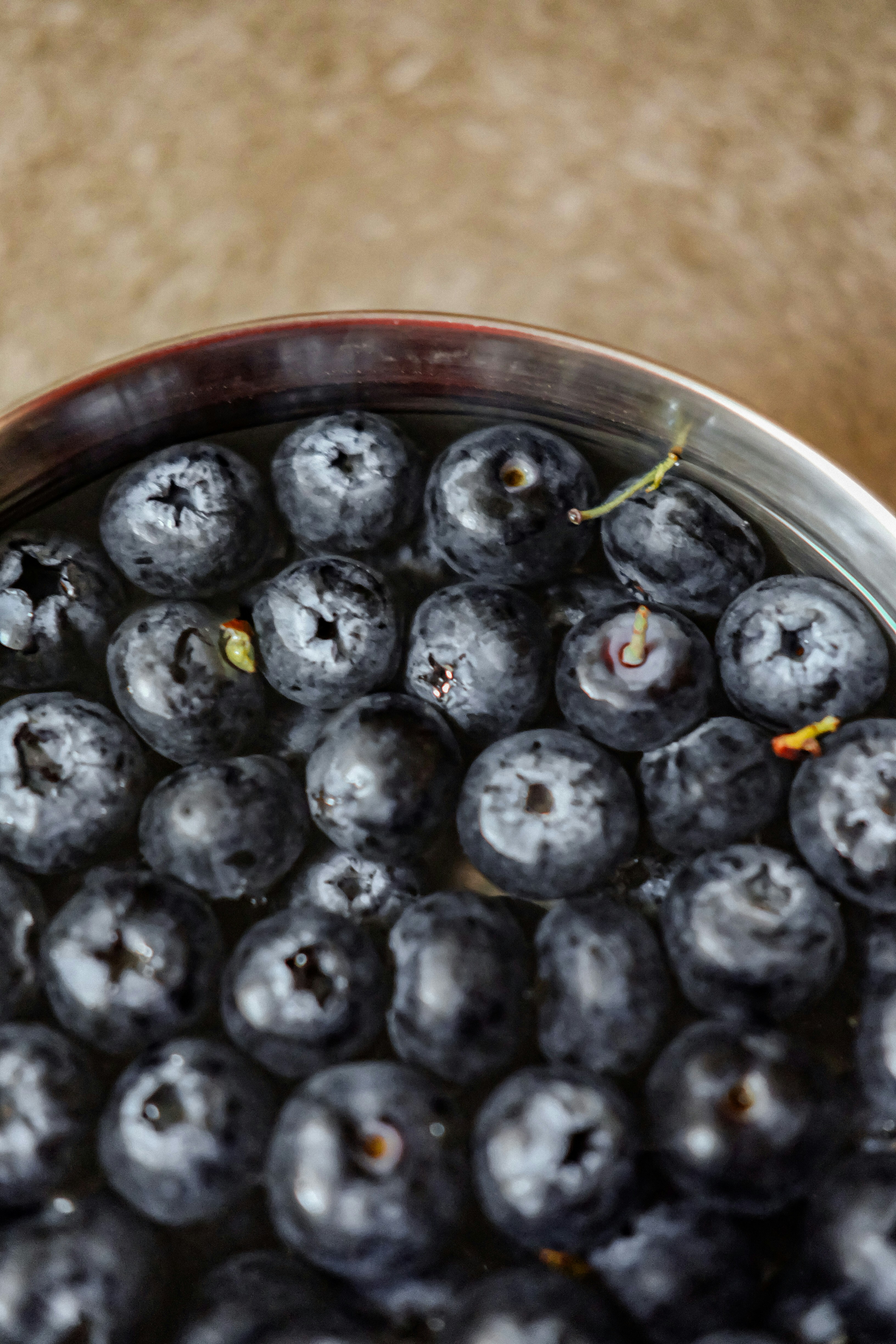 Close-up of a bowl filled with ripe blueberries, highlighting their dusty blue skin and tiny stems against a blurred neutral background.
