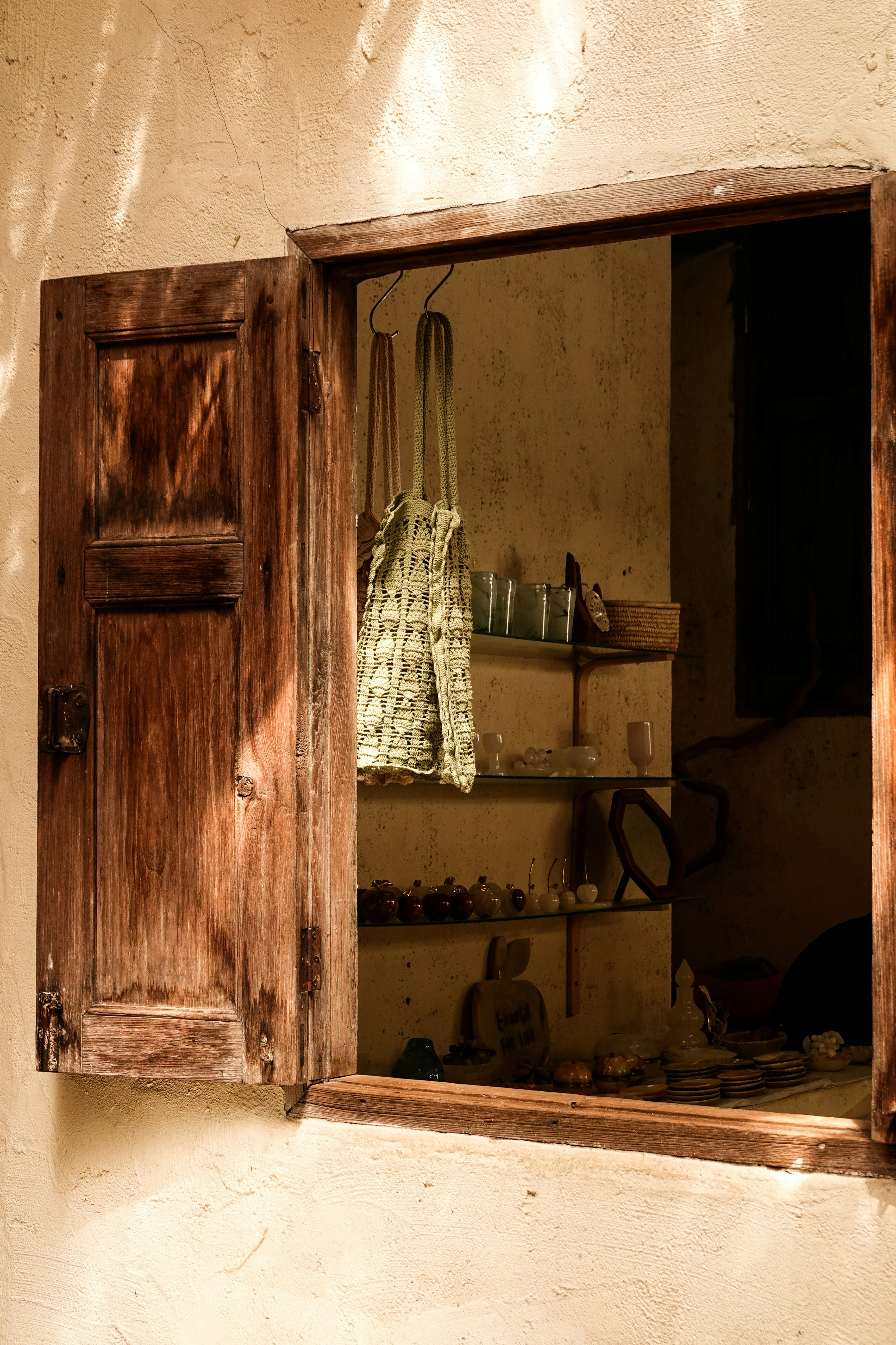 Weathered wooden window with hanging textiles and rustic shelf indoors