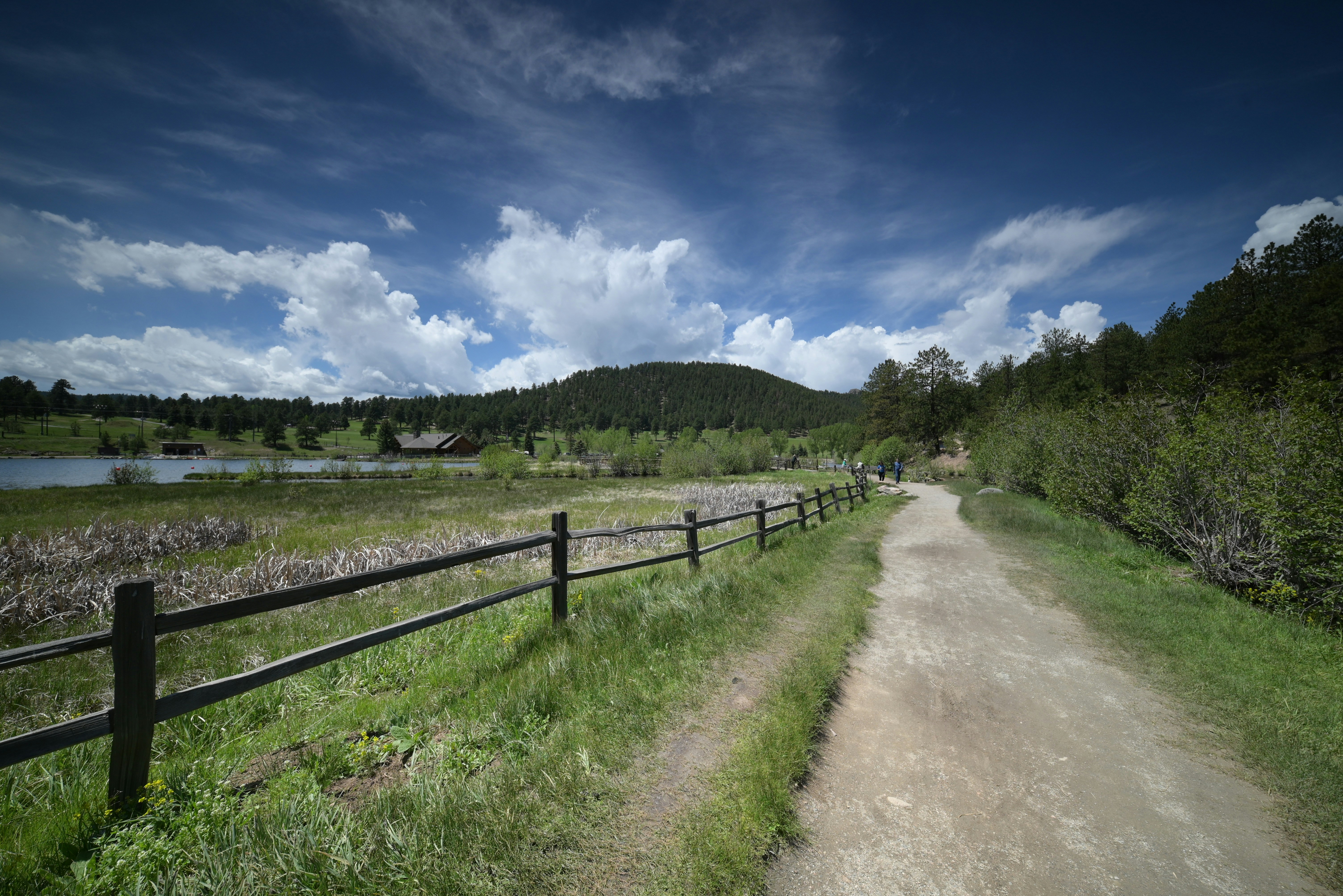 Scenic dirt path, wooden fence, lake, and distant mountains.