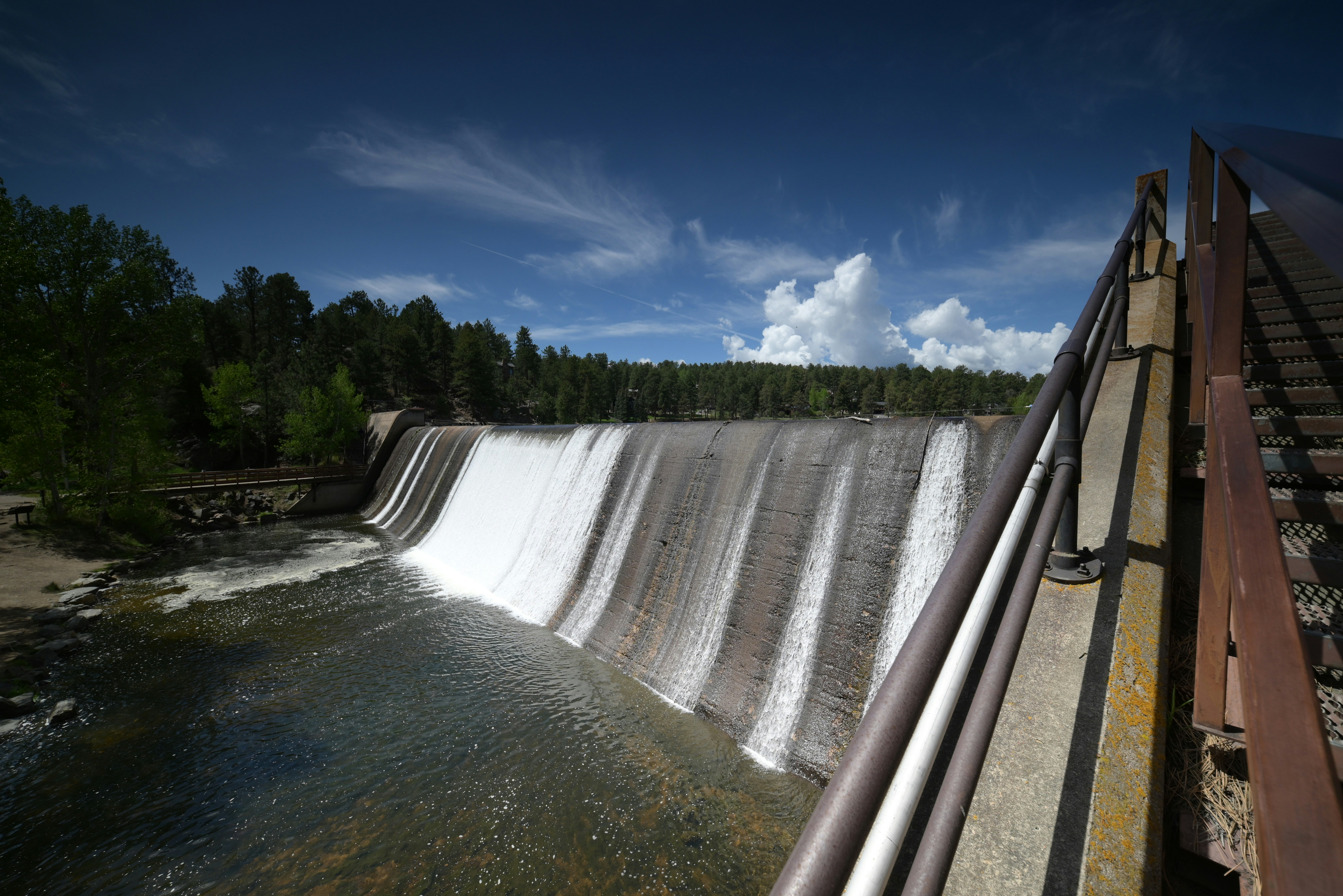 Water cascades over a dam under a bright blue sky.