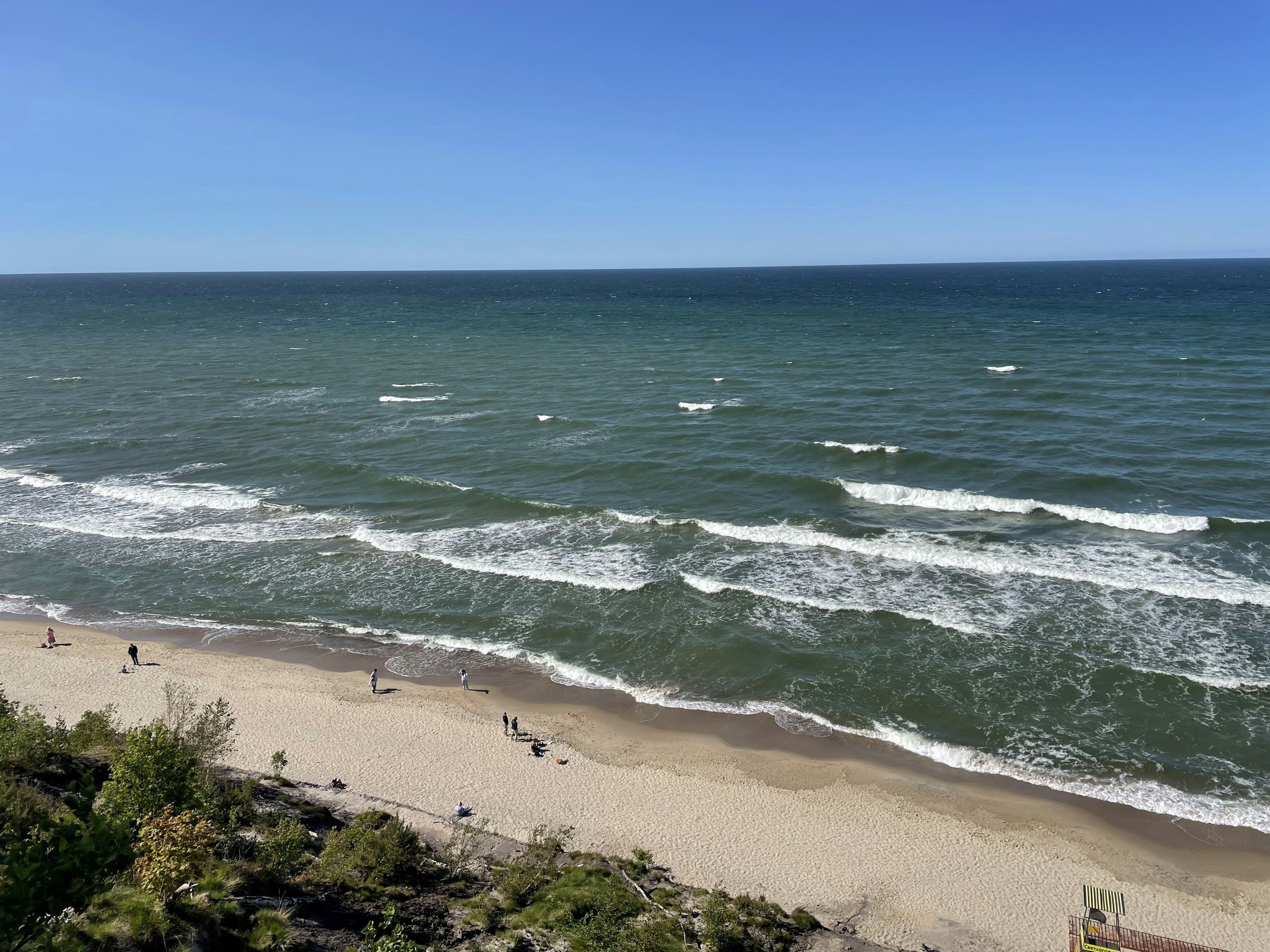 Sunlit Shoreline: Gentle Waves and Distant Beachgoers