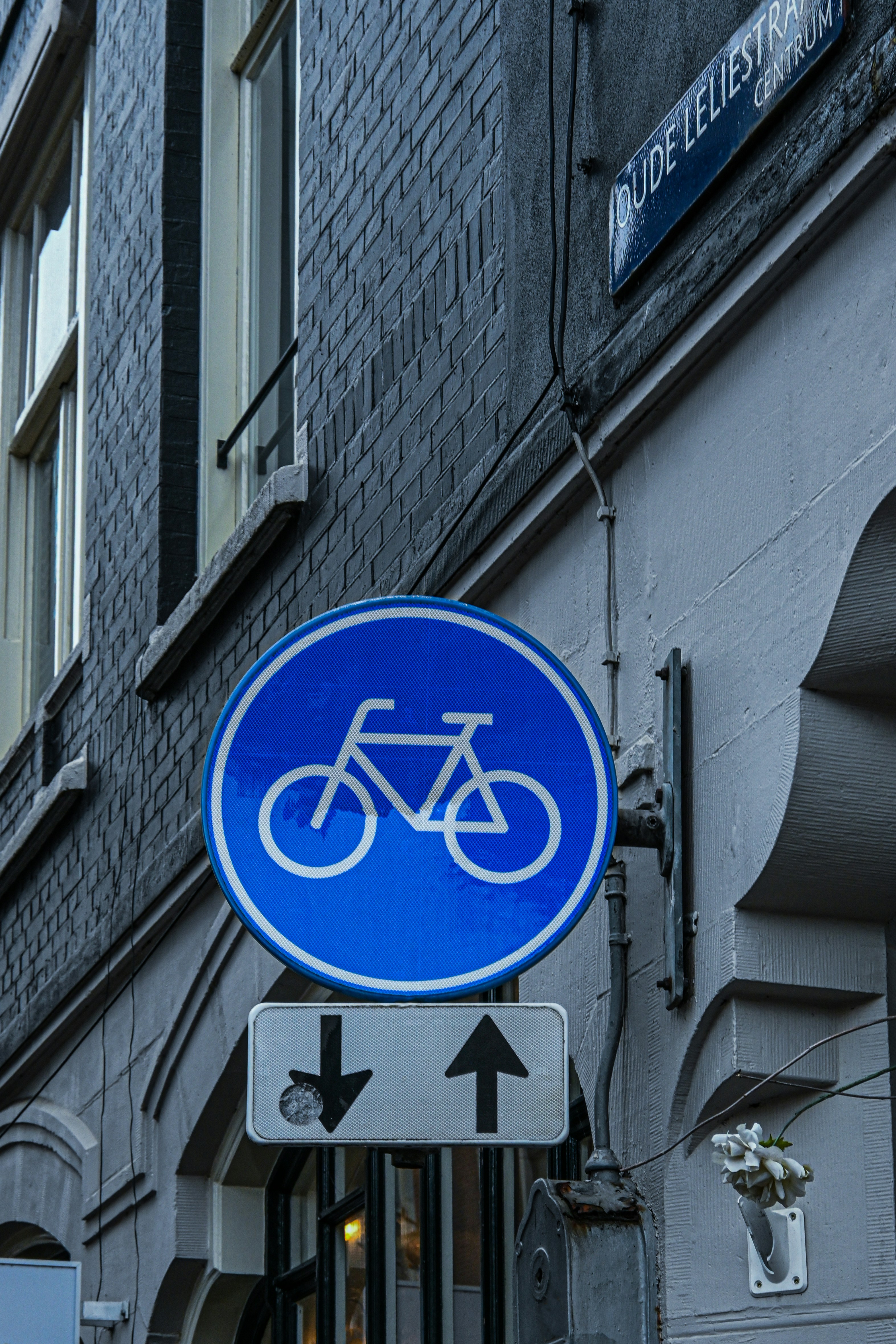 Blue bicycle sign and directional arrows on a grey building.