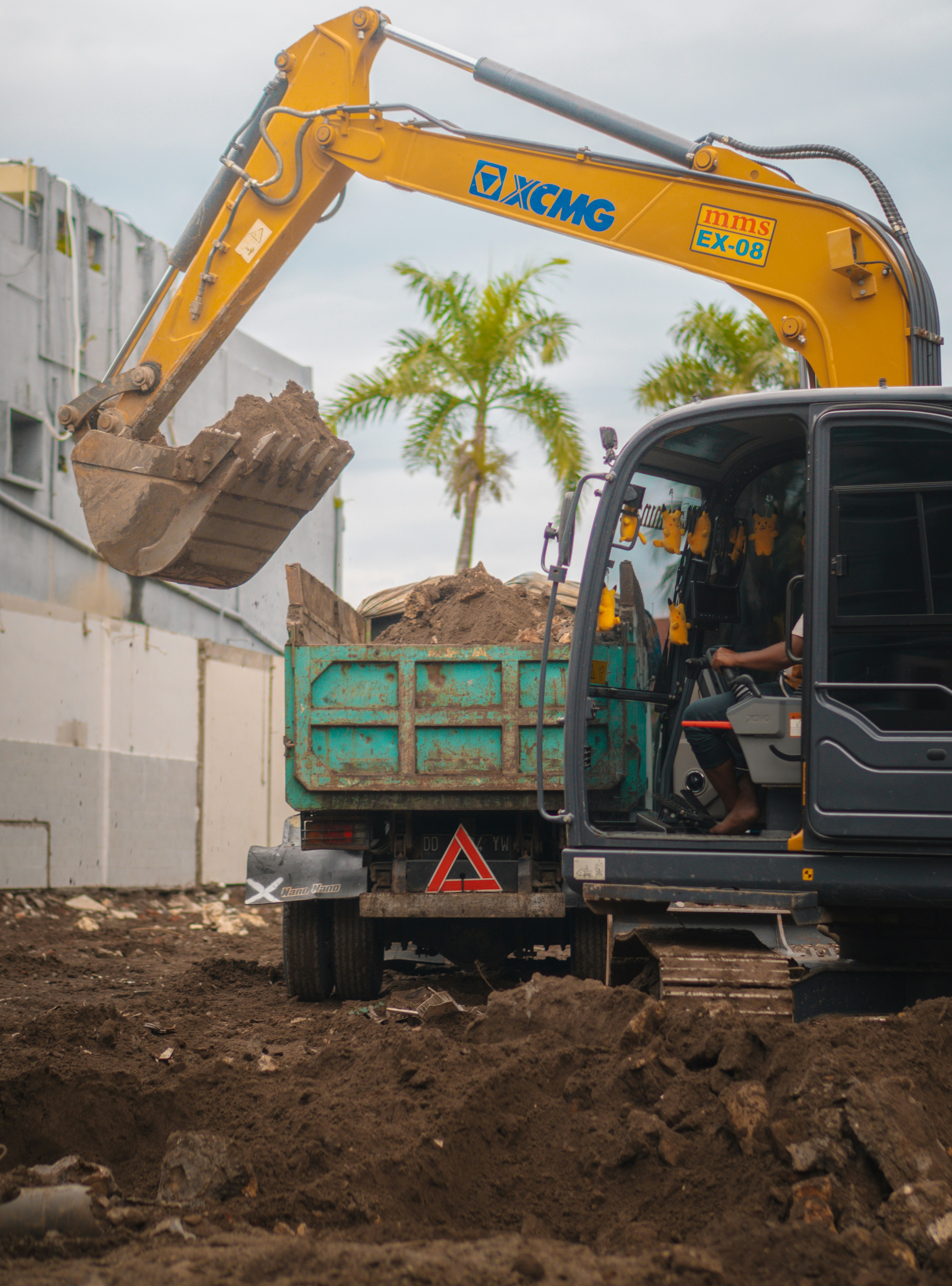 A yellow excavator loads dirt into a green dump truck.