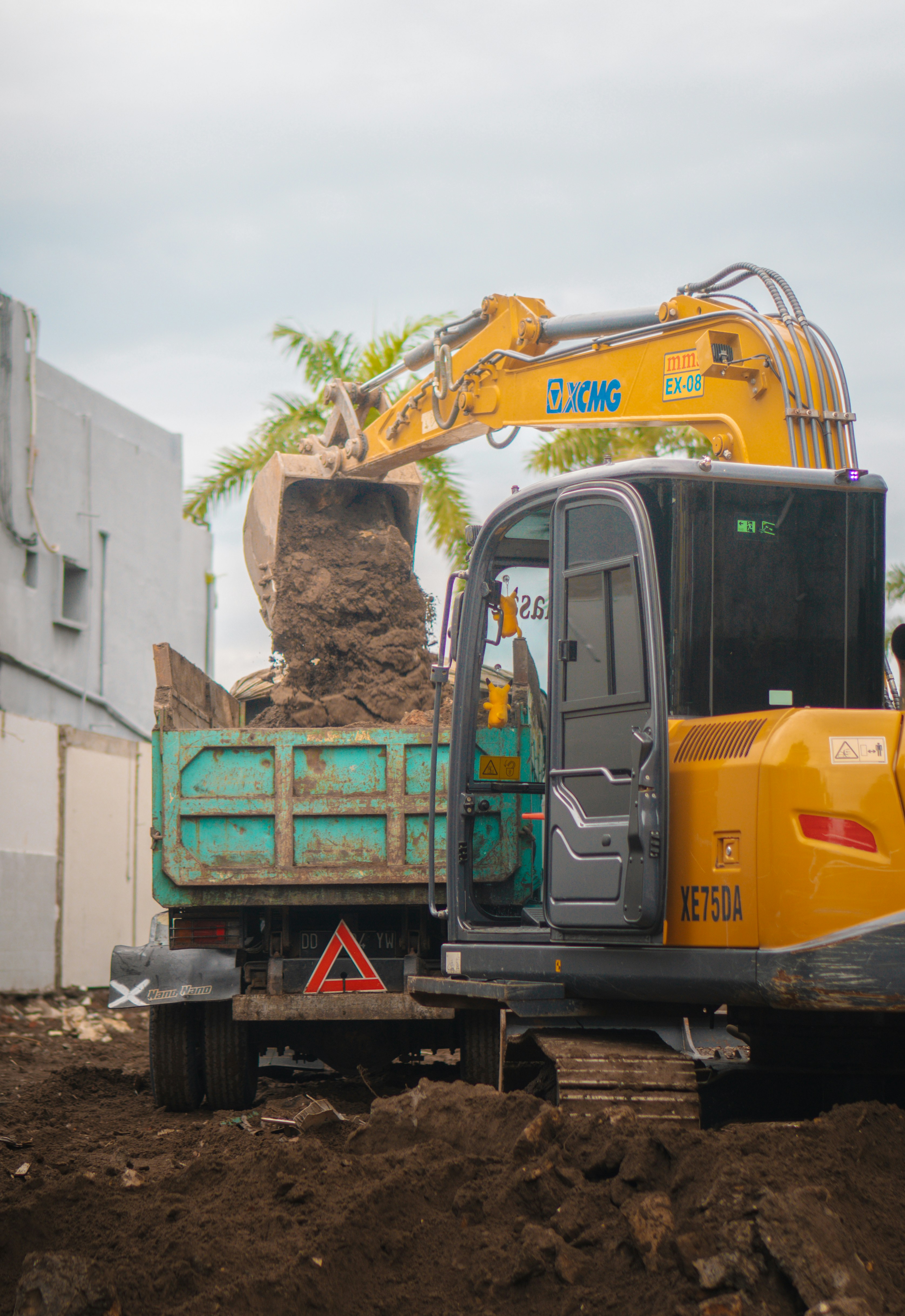 A yellow excavator loads dirt into a green dump truck.