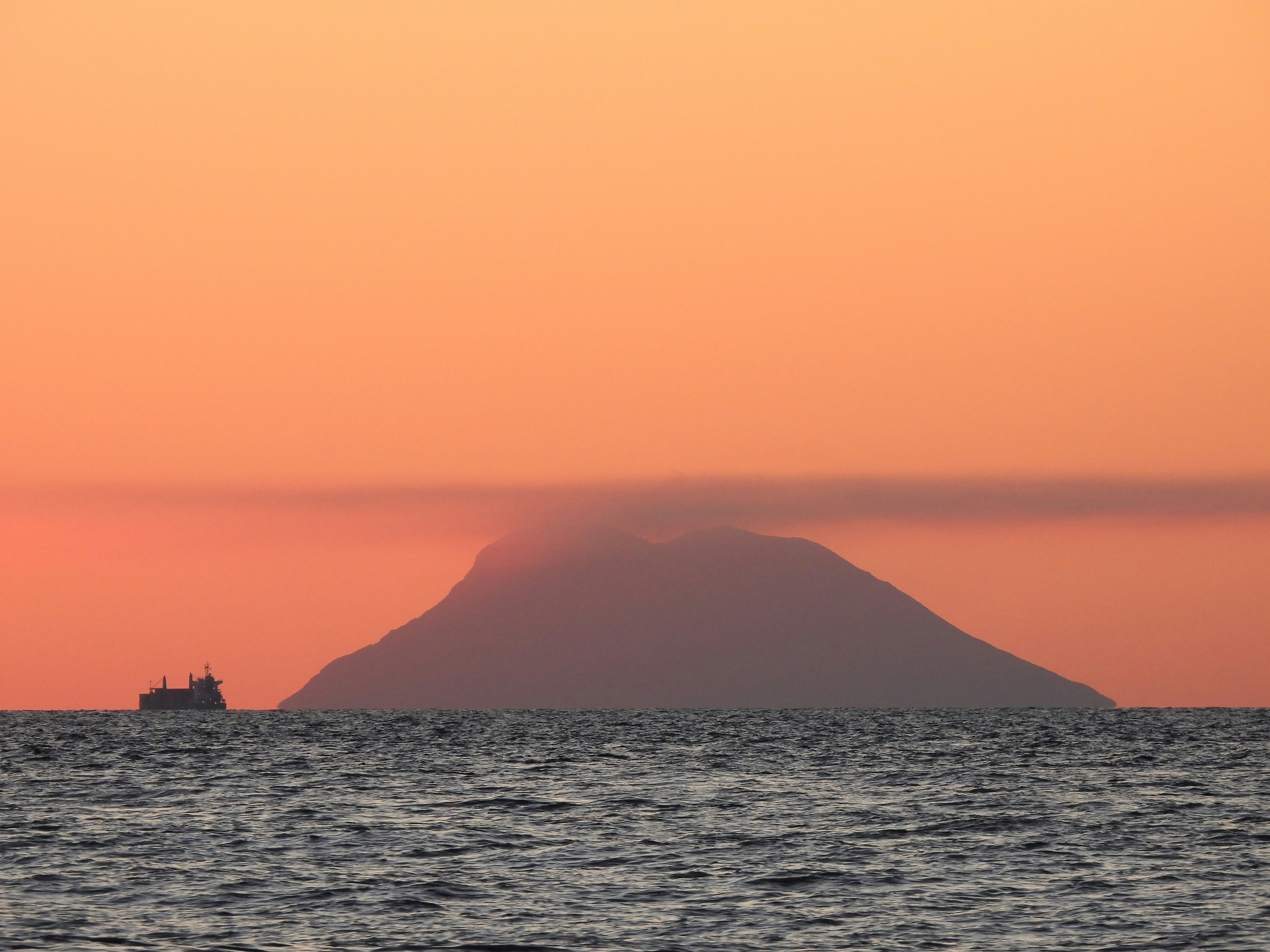 Distant Island at Sunset with a Silhouetted Vessel