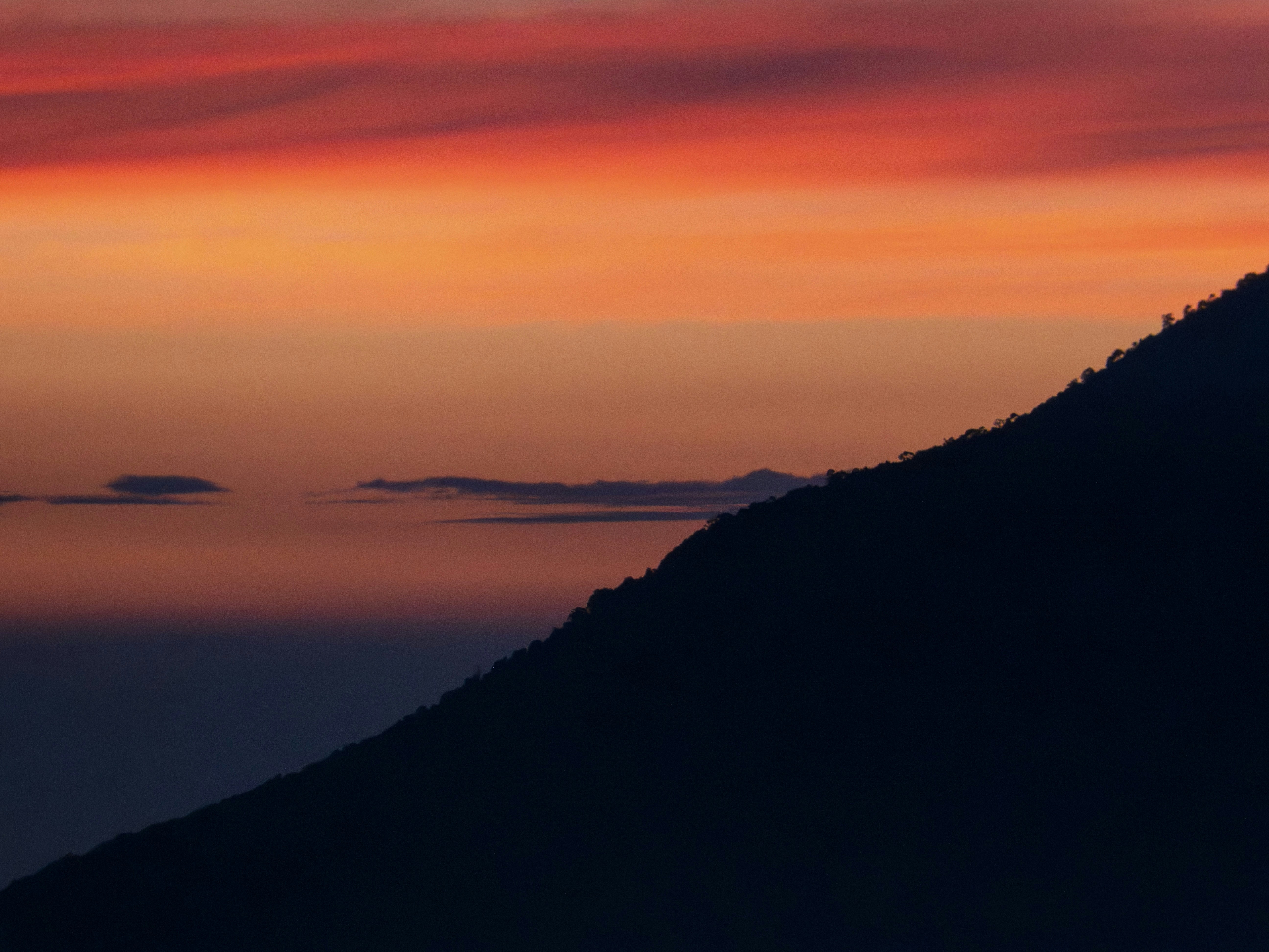 Silhouette of a mountain ridge against a vibrant sunset sky with warm oranges and deep blues; a landscape composition emphasizing horizon line and color gradient. (photograph) 