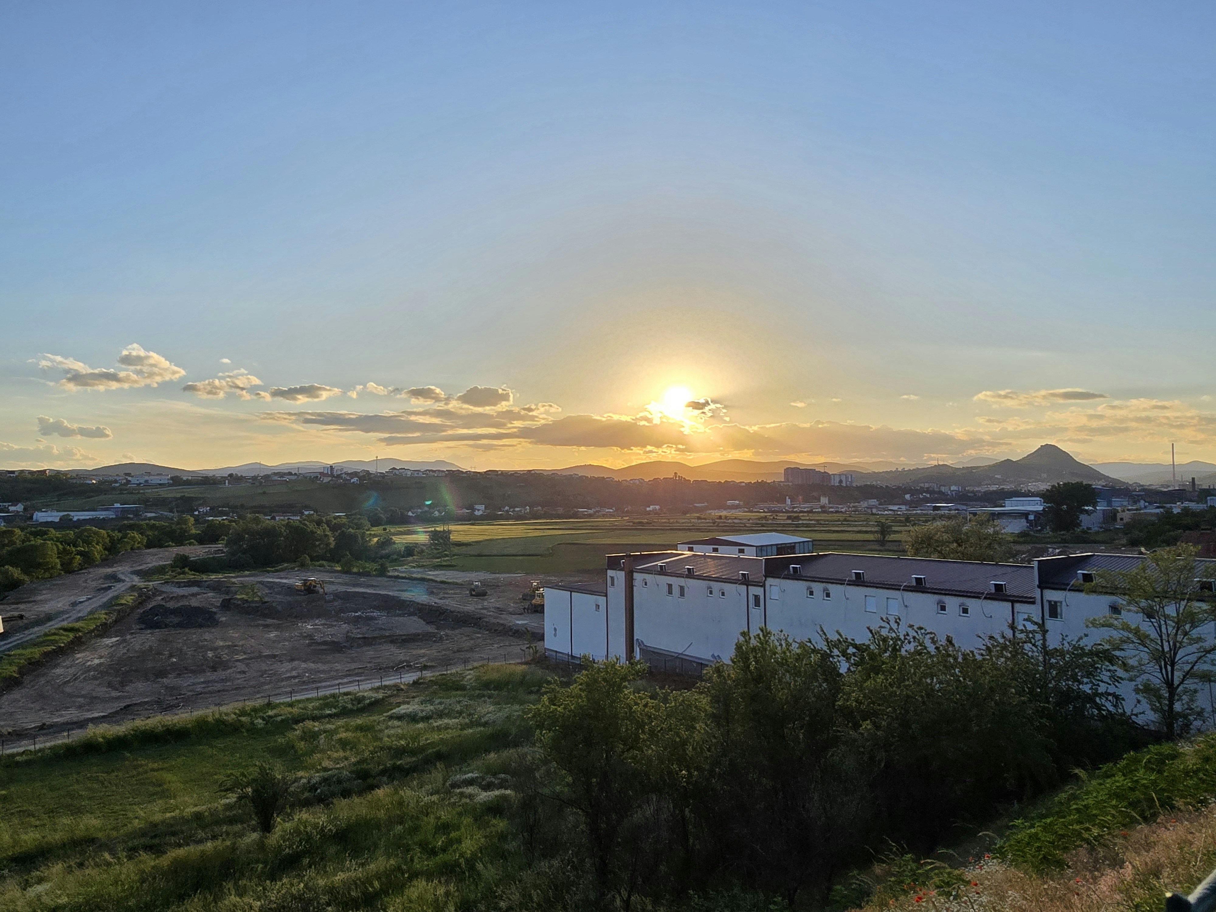 Sunset Over Mixed Landscape: Factory, Fields, and Distant Volcanic Silhouette
