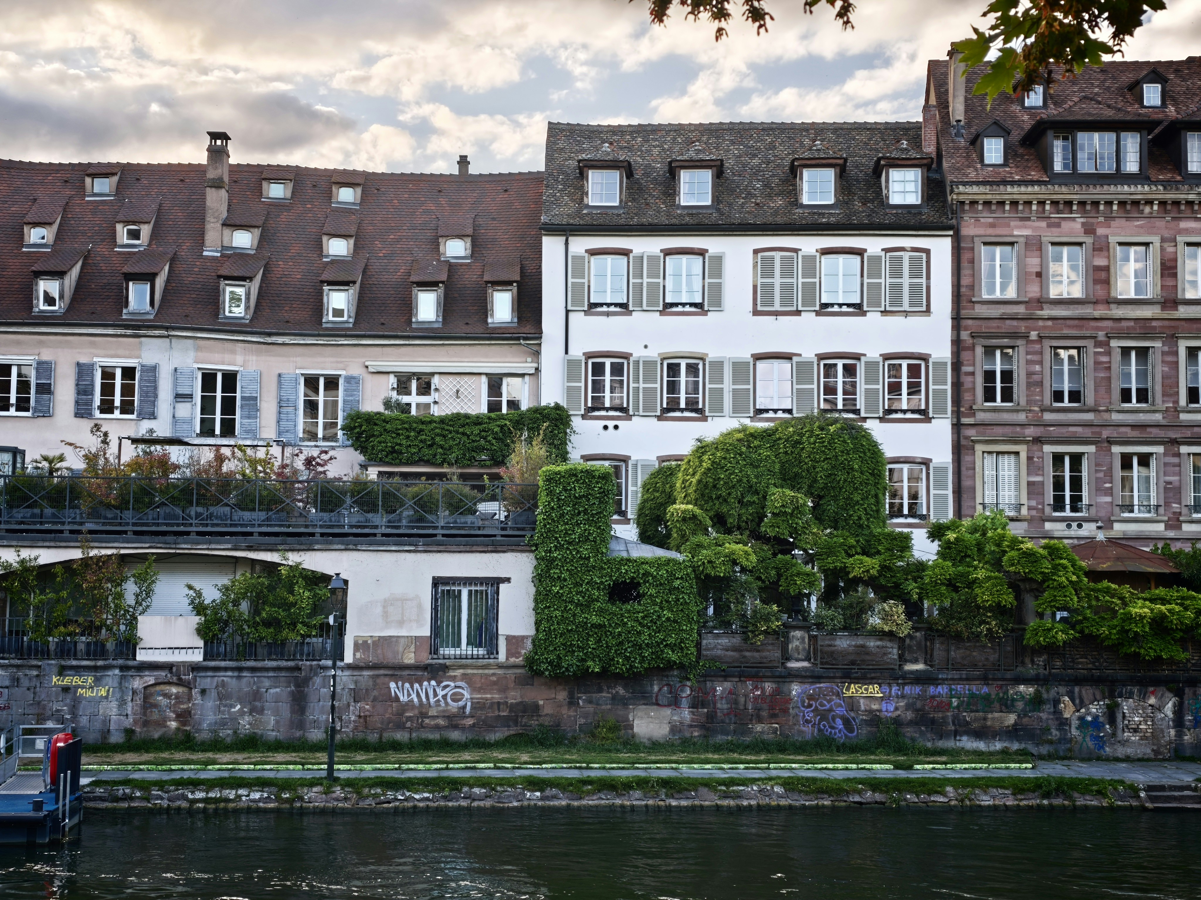 Row of pastel houses along a calm riverbank framed by trimmed greenery