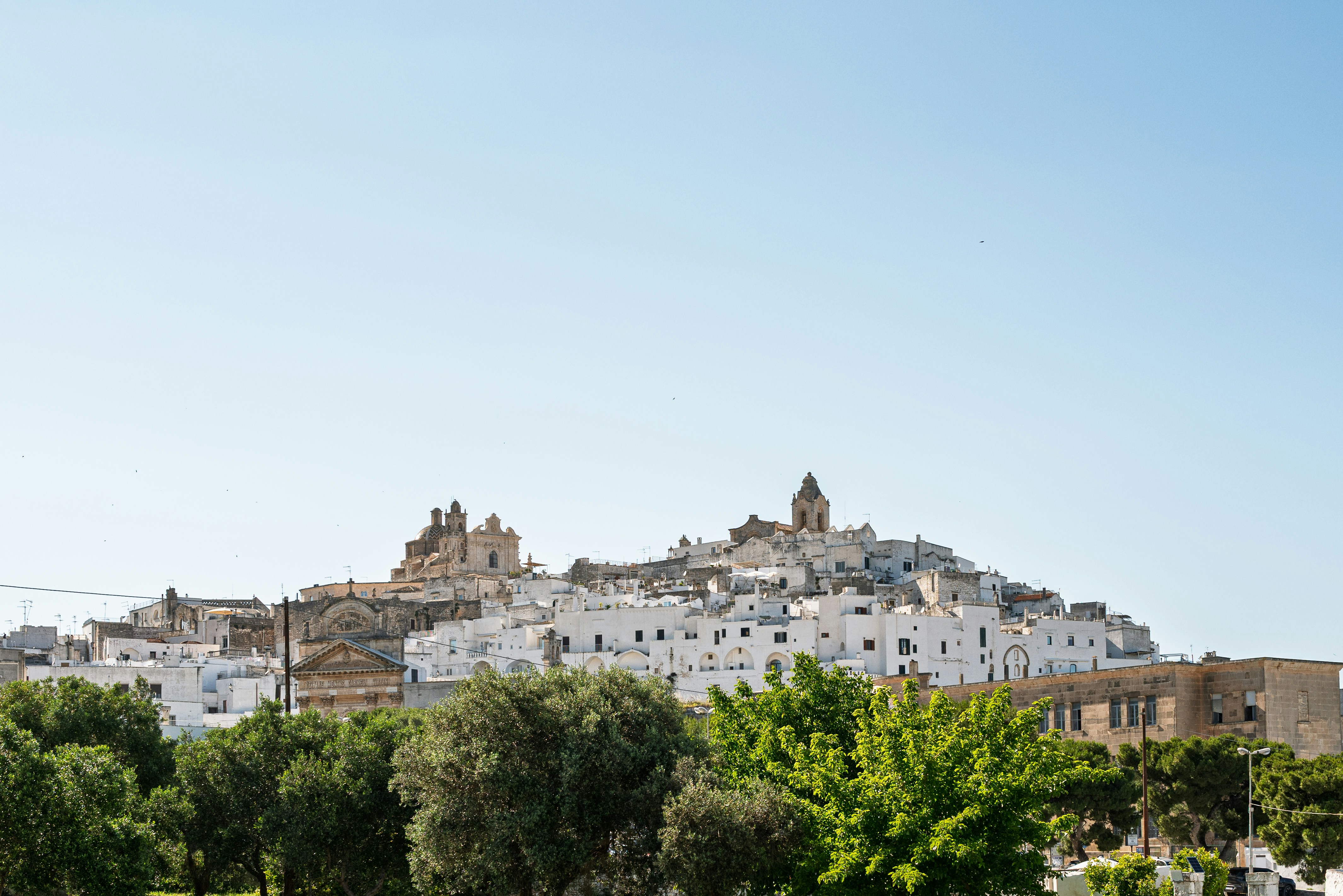 White hilltop town with historic buildings and green trees.