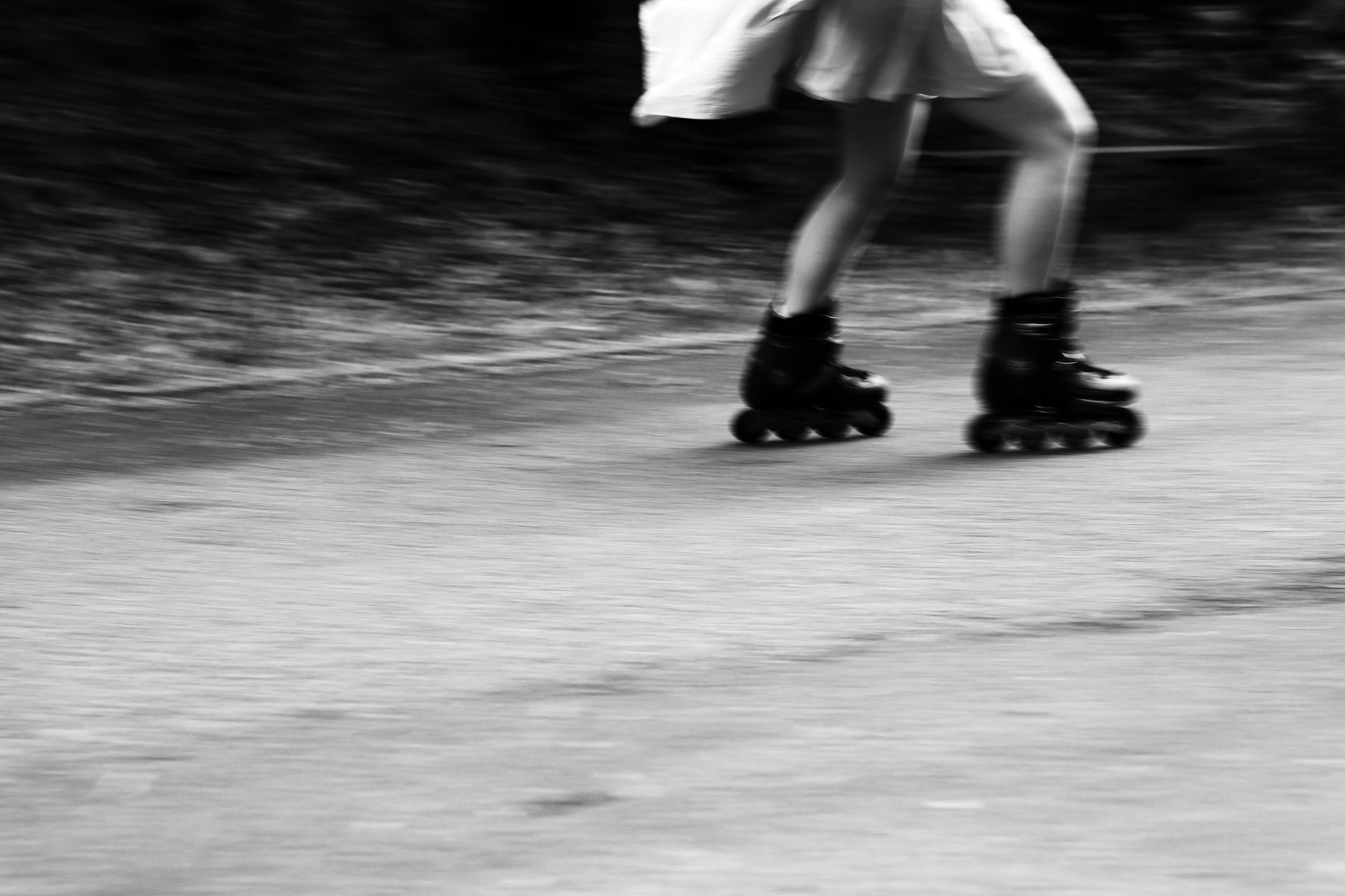 Motion blur of a skater on inline skates across a sunlit path, emphasizing movement and speed without facial detail. A simple, high-contrast monochrome capture with a focus on the leg action.