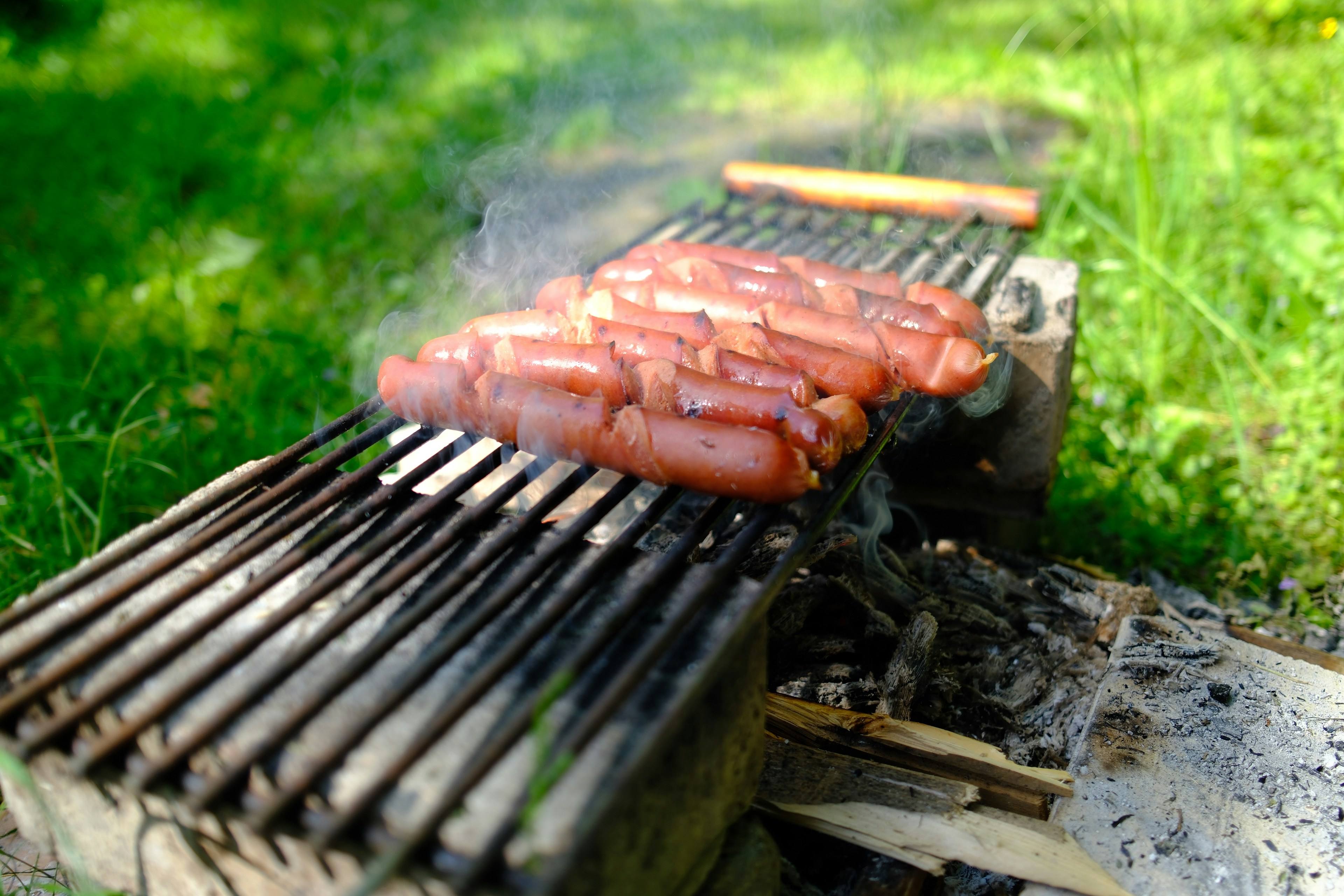 Sausages cooking on an outdoor grill with smoke.